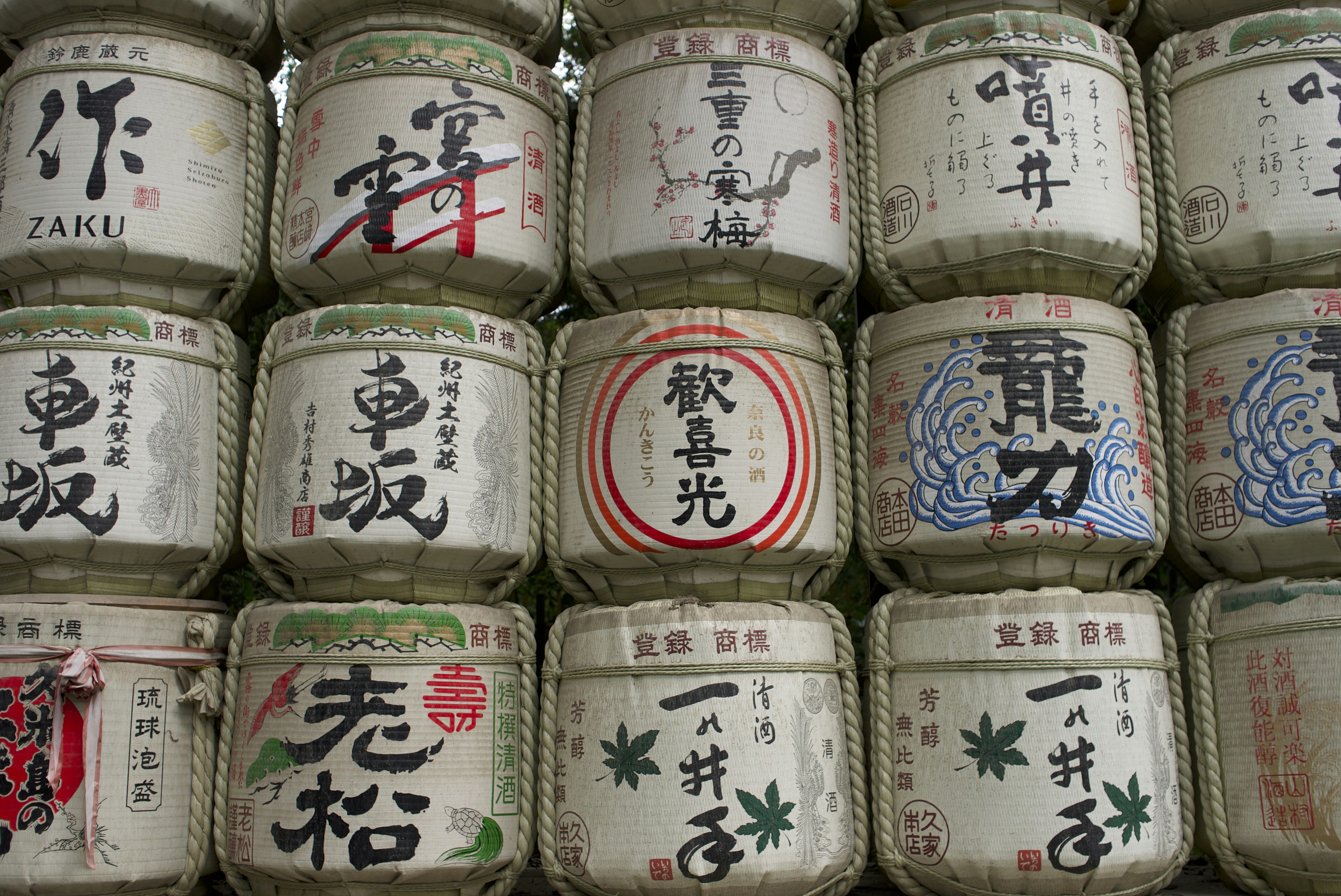 Rows of ceramic sake barrels with Japanese calligraphy line a wall, each barrel showing unique characters and artwork for a traditional display.