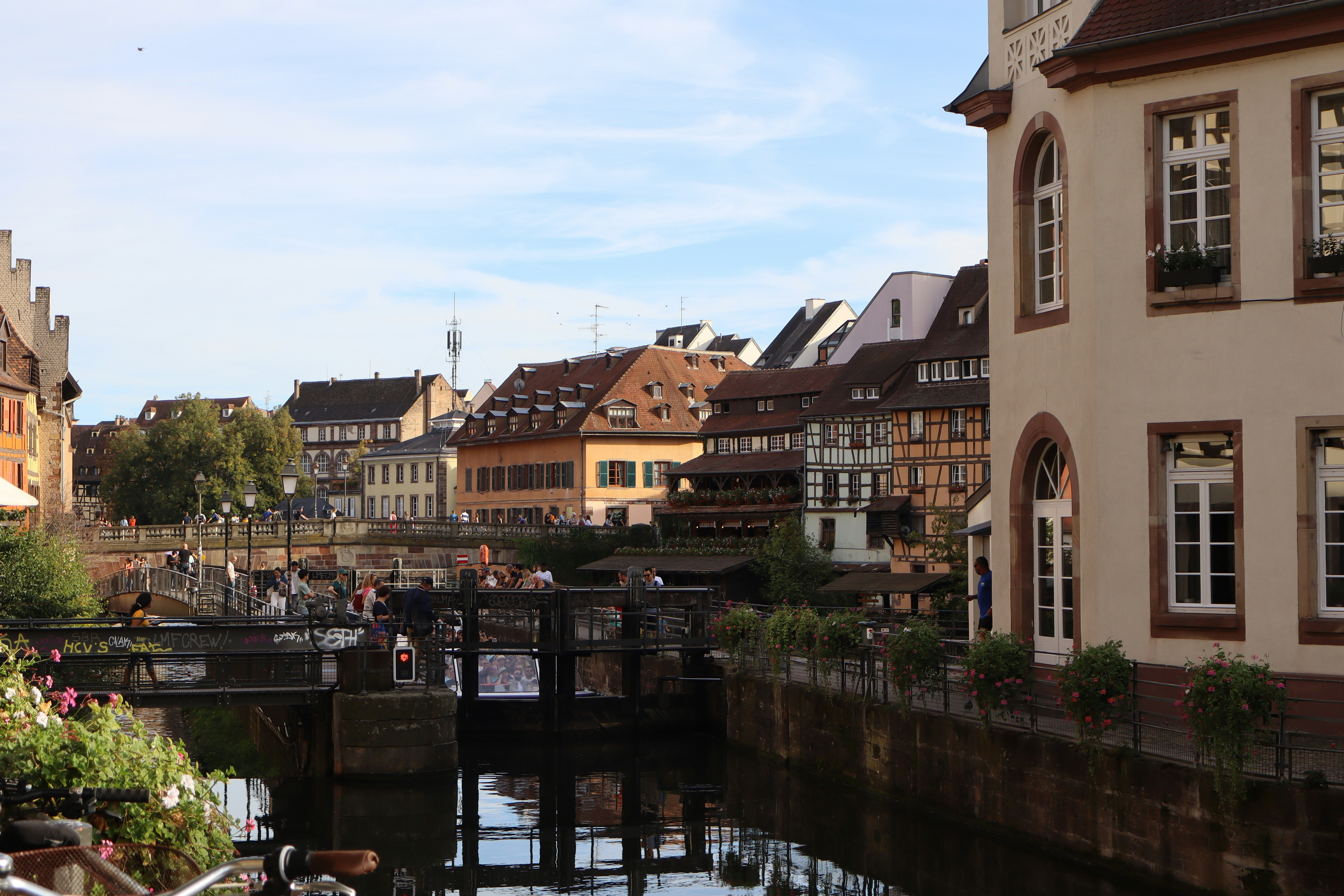 Colorful canal-side village with a row of timber-framed buildings and a small bridge over calm water.