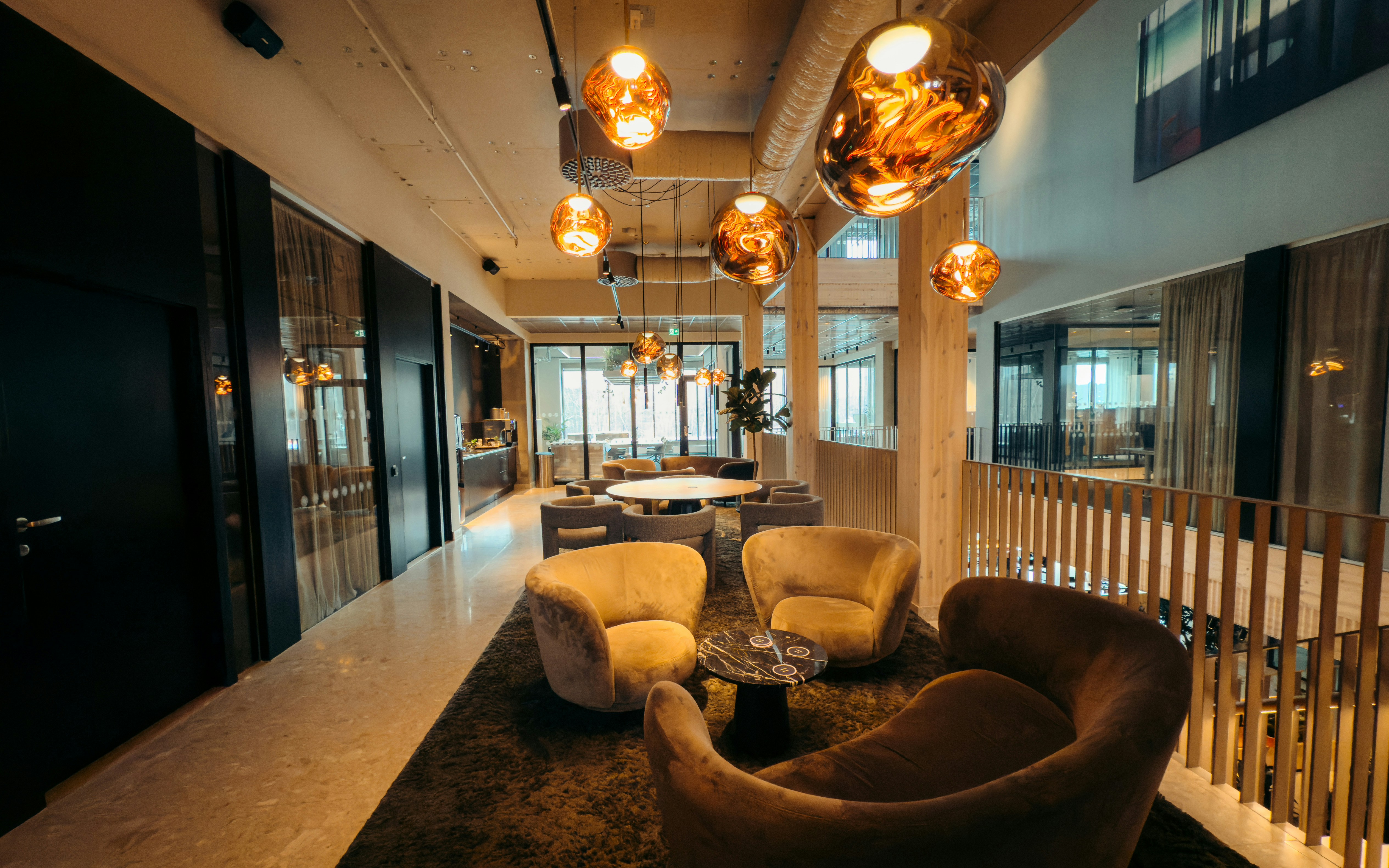 Warm, inviting lounge area with plush seating and copper pendant lights in a modern office setting.