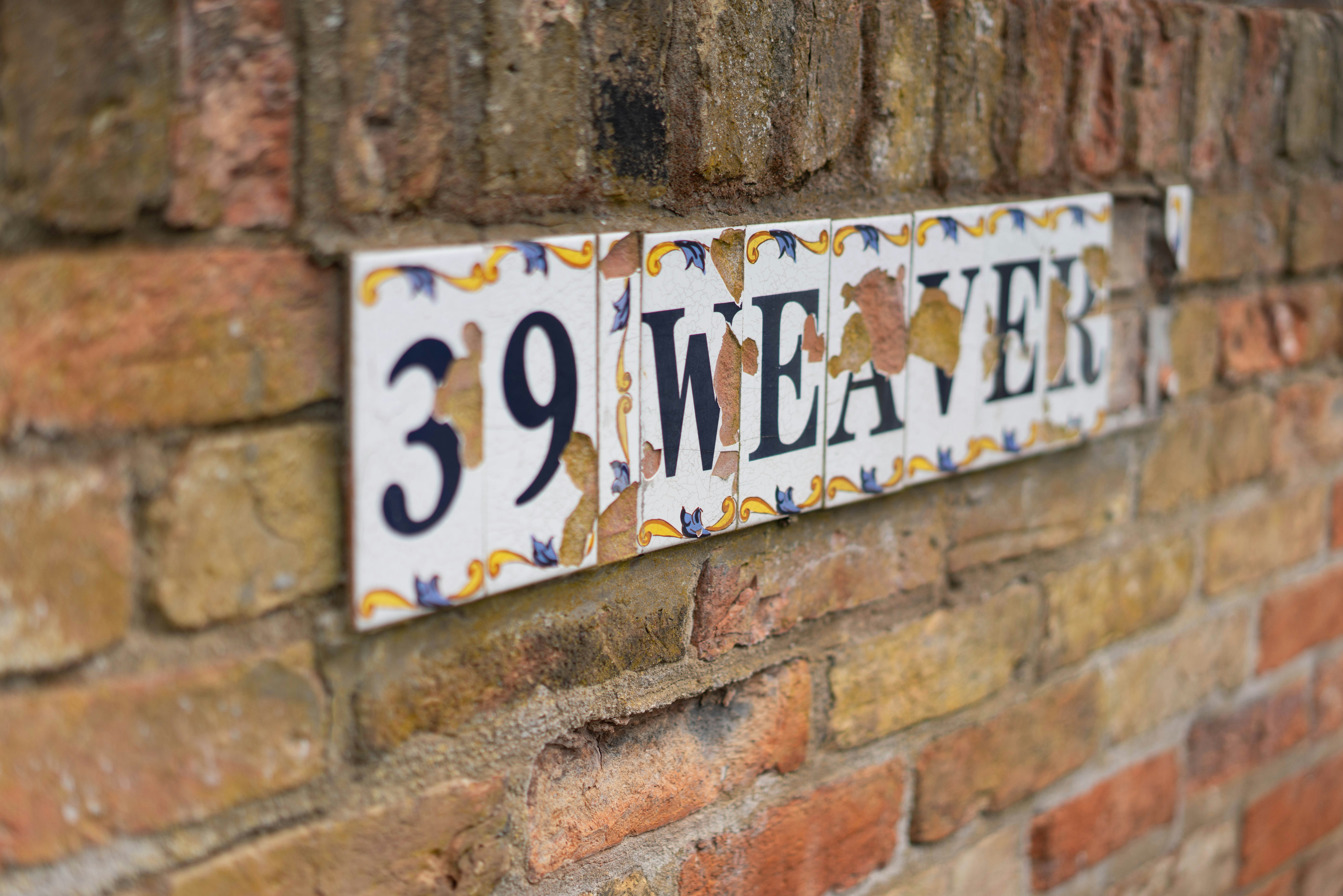 Weathered ceramic tiles reading 39 WEAVER mounted on a rustic red brick wall
