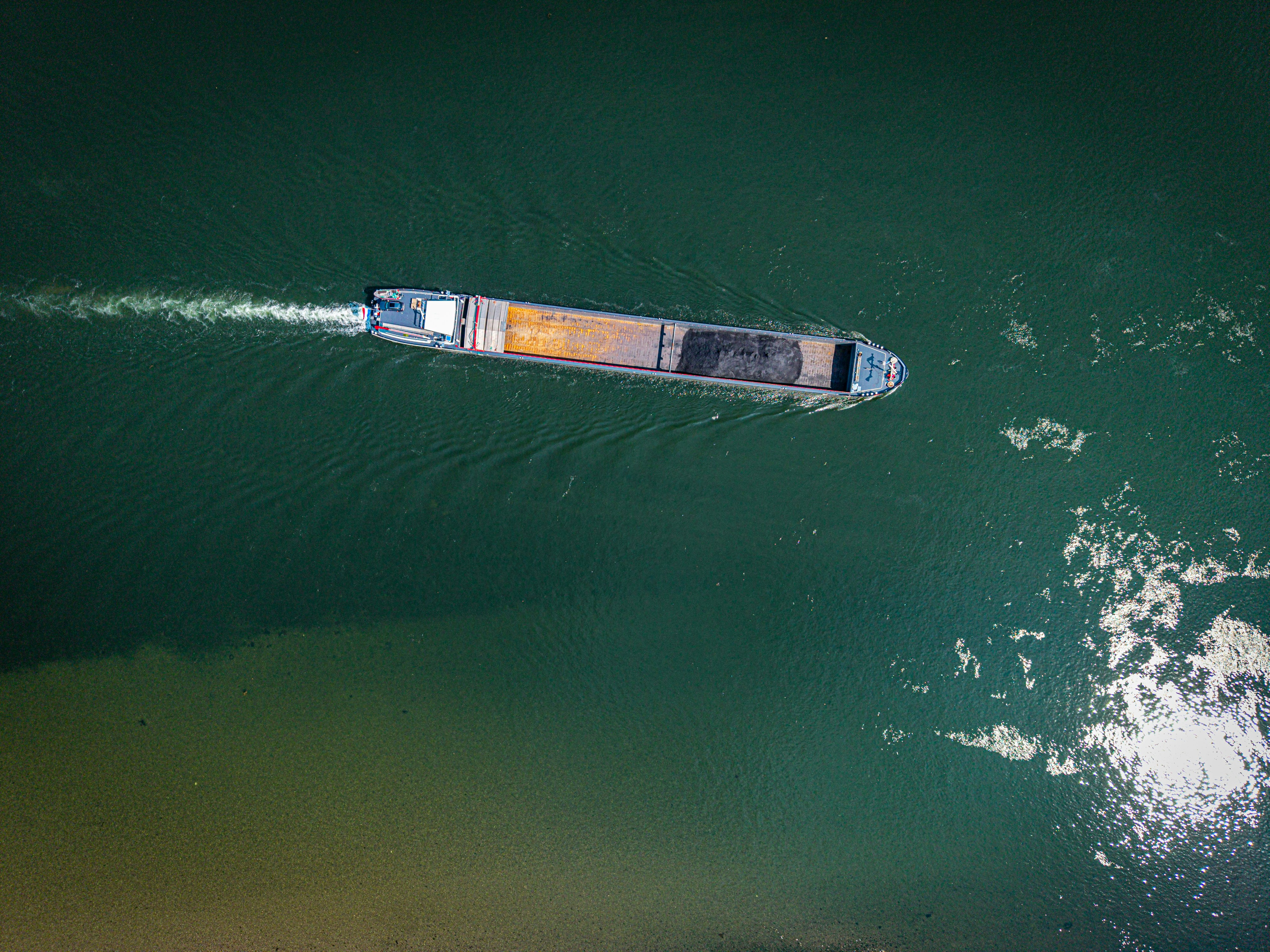 Midday Passage: A lone cargo boat gliding through sunlit green waters