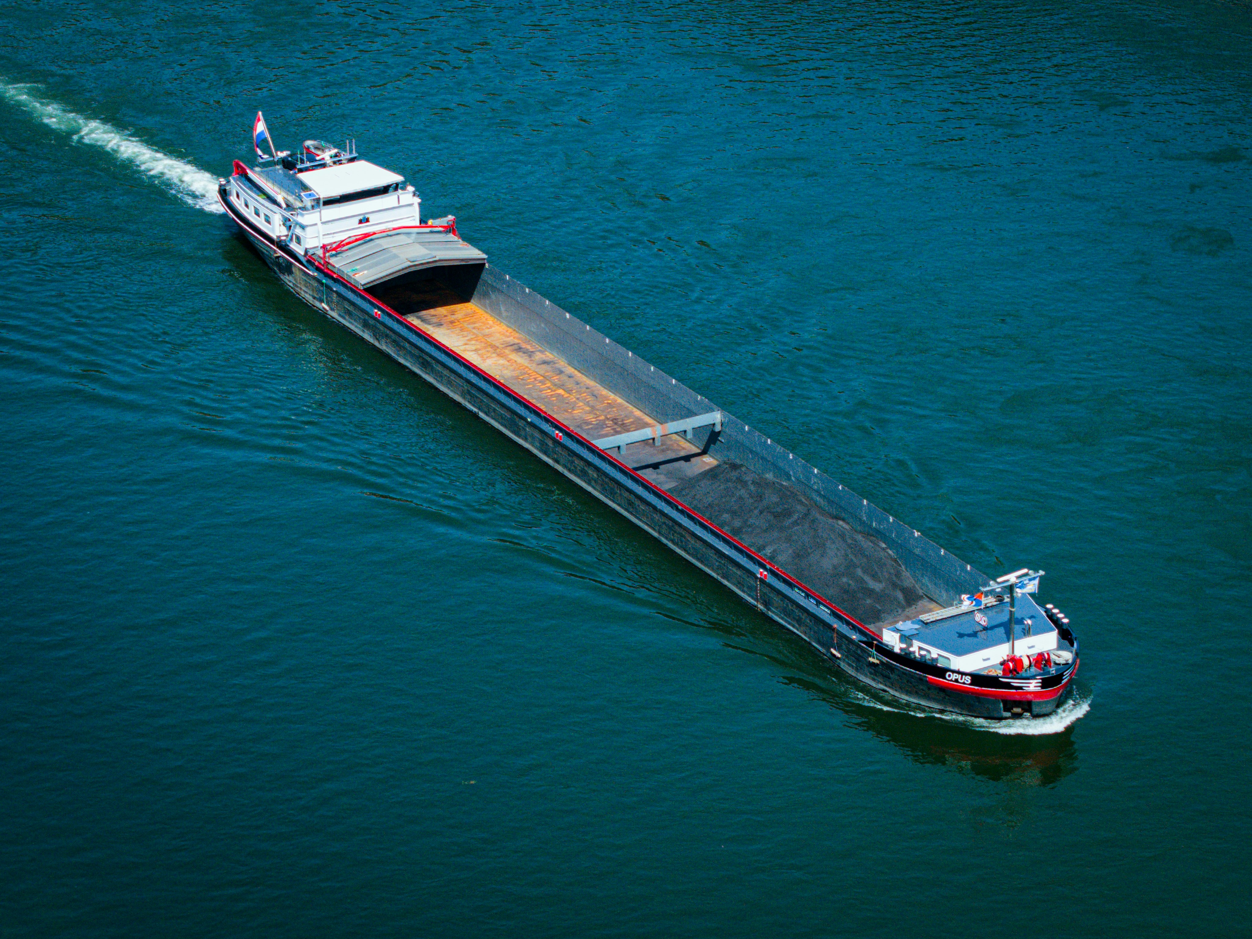 Aerial Tow: Blue-green Wake Carries a Long Barged Contender