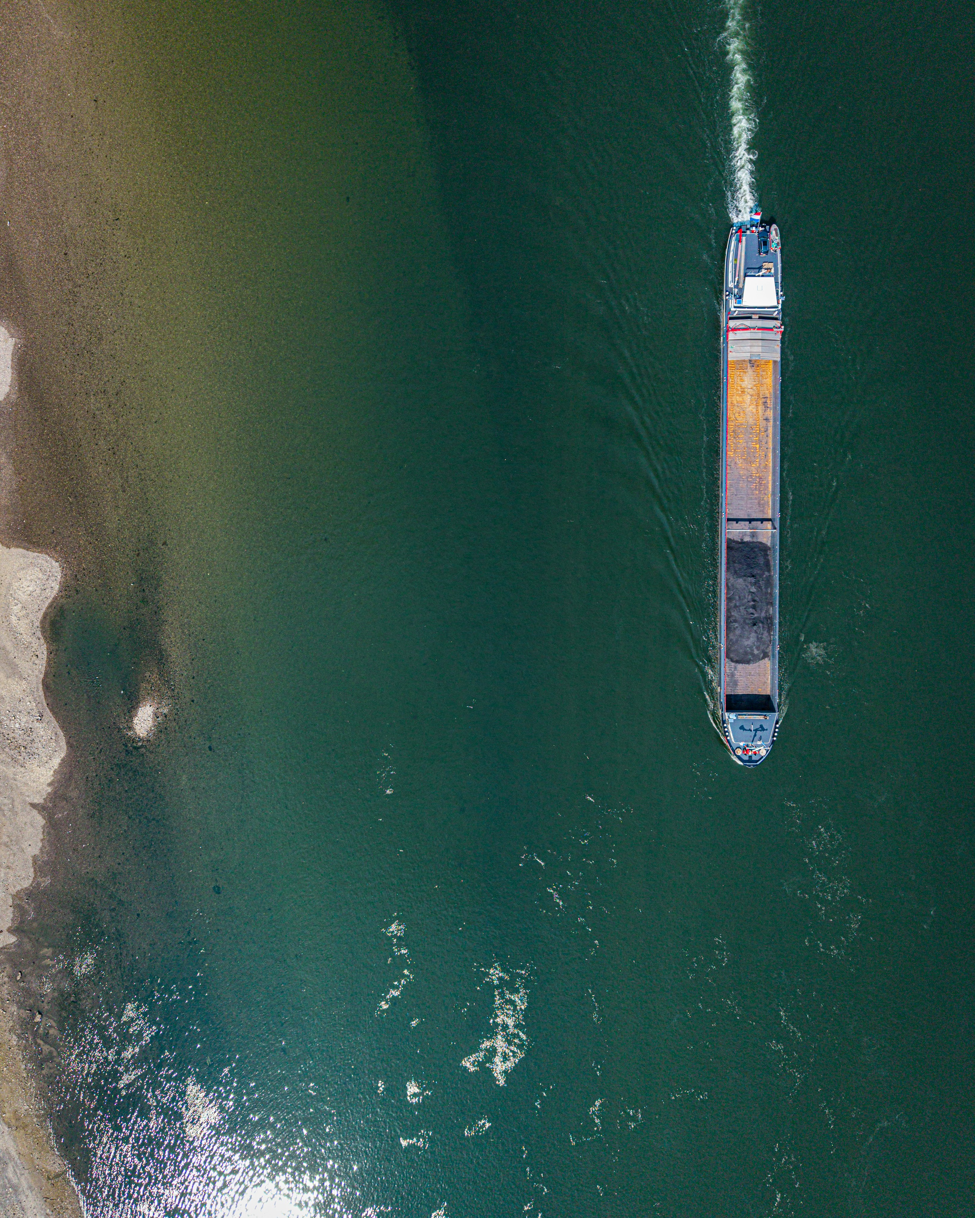 Aerial freight: vessel traces a straight wake along a green shoreline