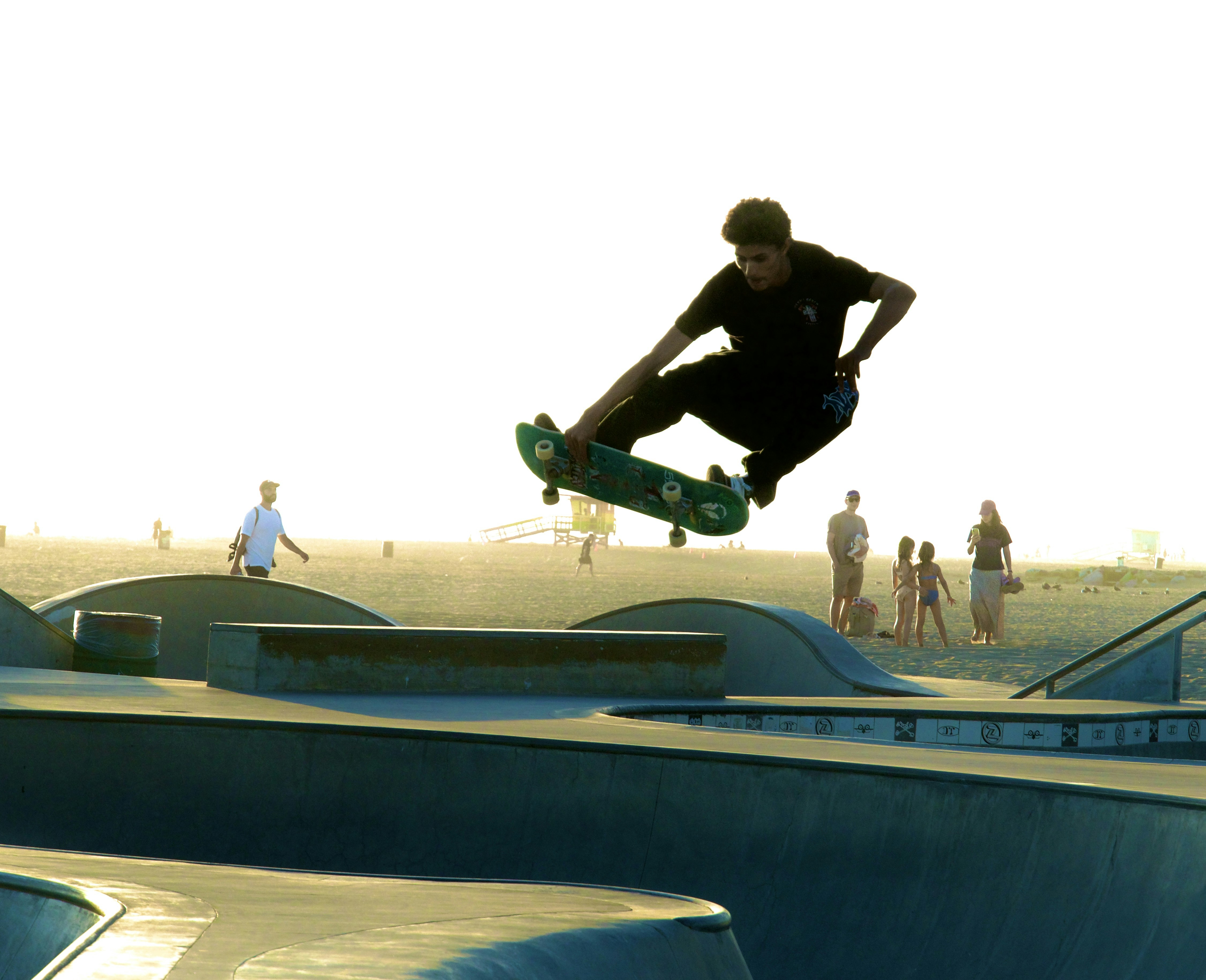 A person jumping on a skateboard at a concrete skatepark during golden hour