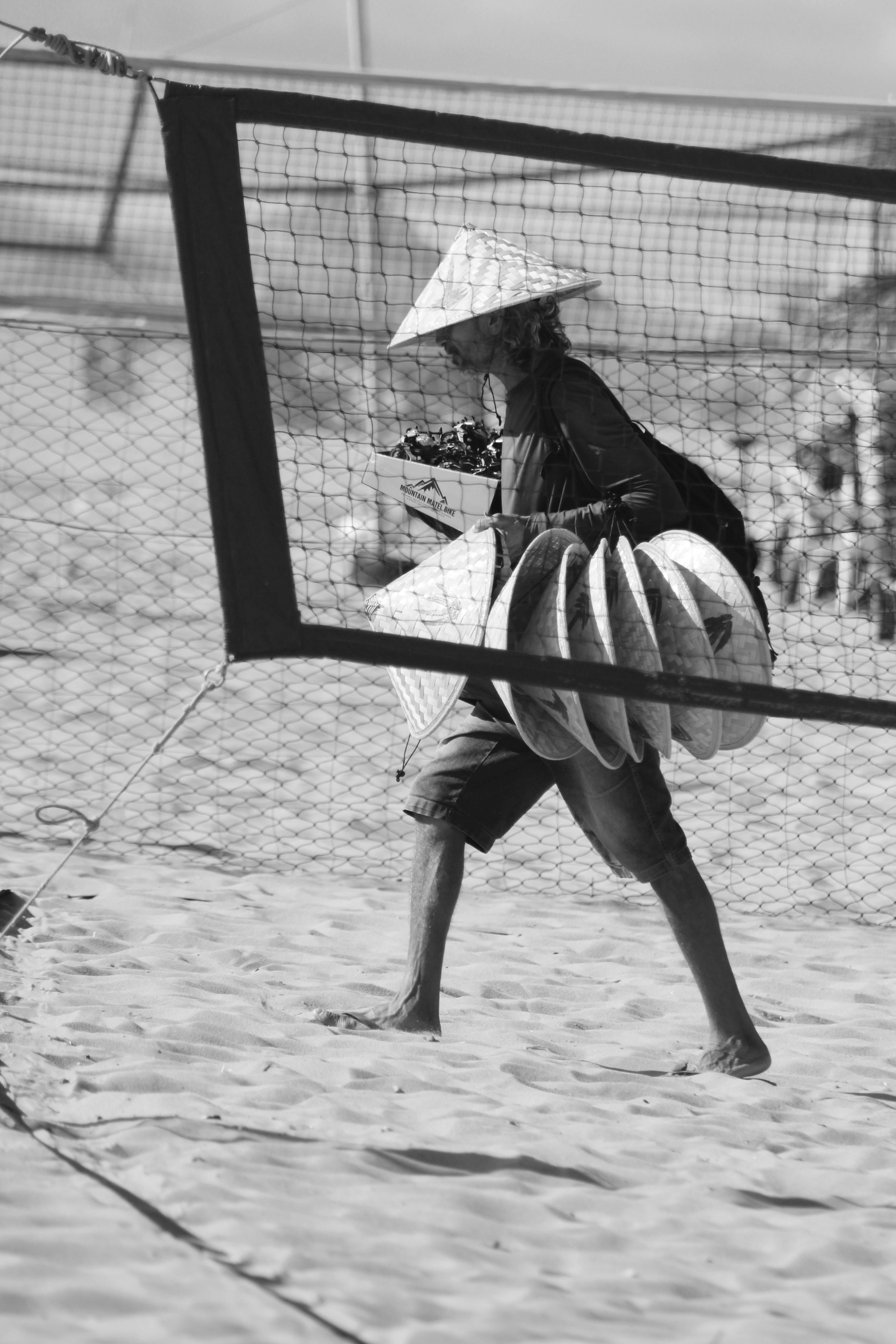 Beach vendor carrying a woven tray and mesh frame across the shoreline