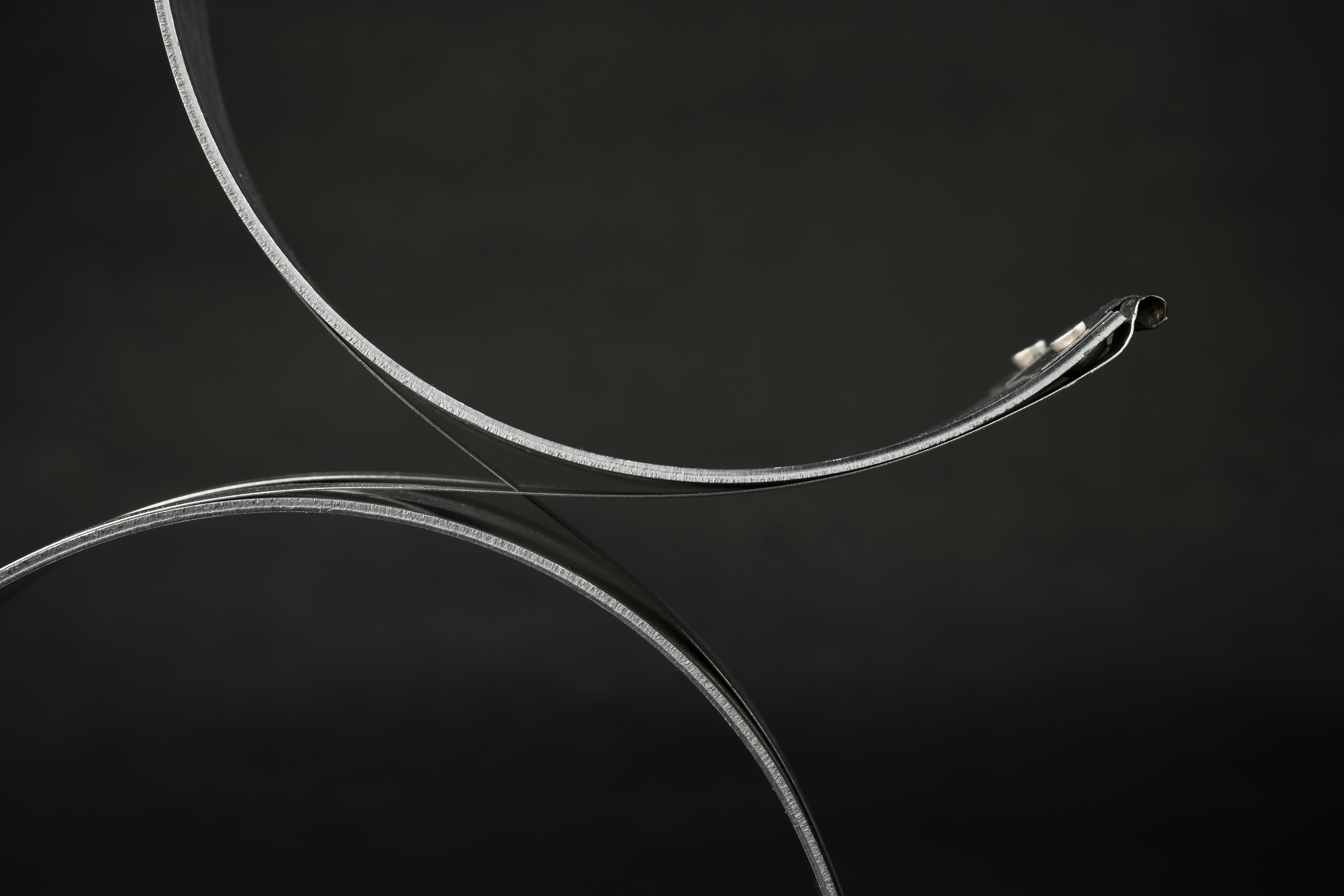 Curved wire ballet: a suspended curve threads a lone glinting tip