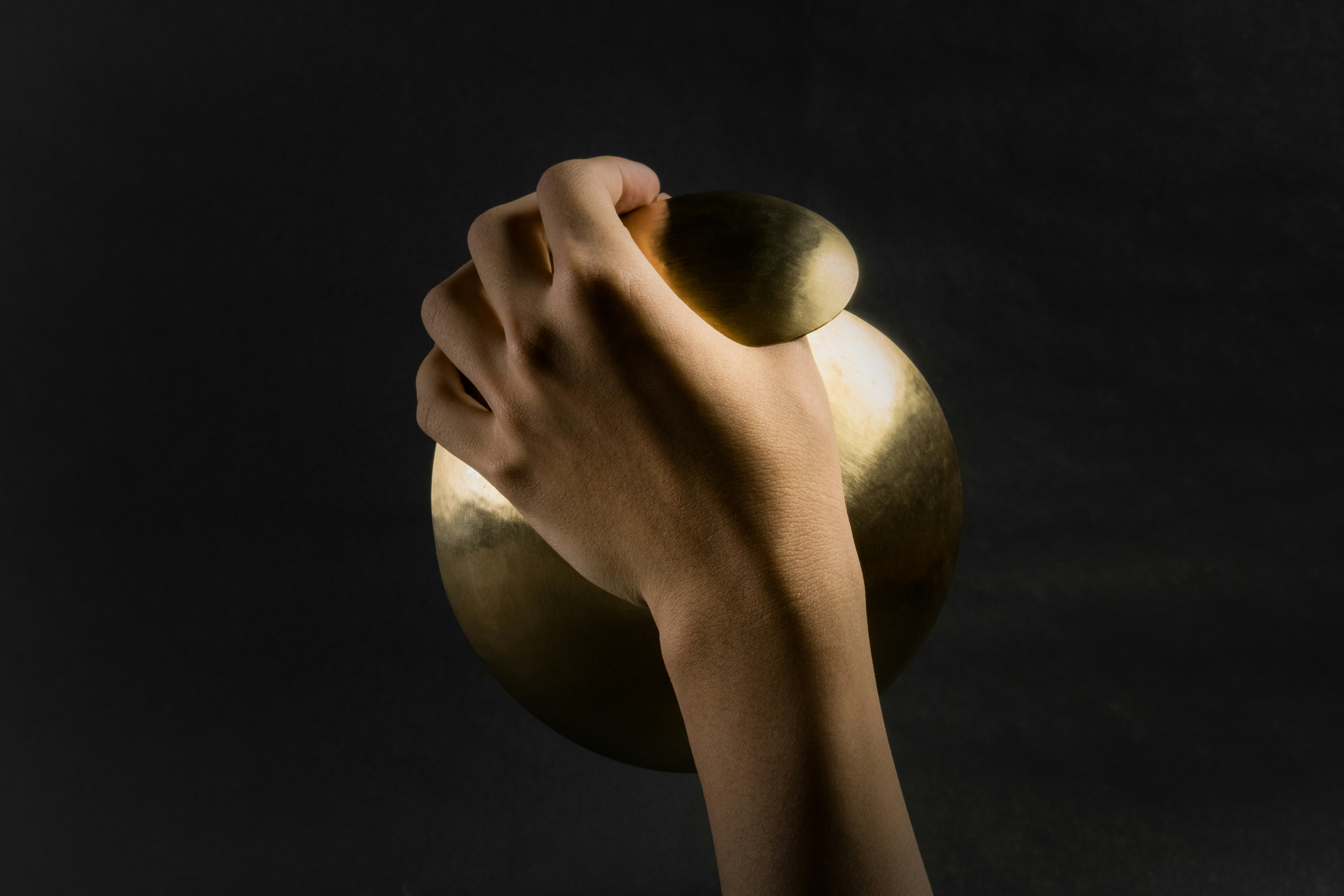 Gilded Grip: A Hand Grasping a Brass Sphere Against Velvet Darkness