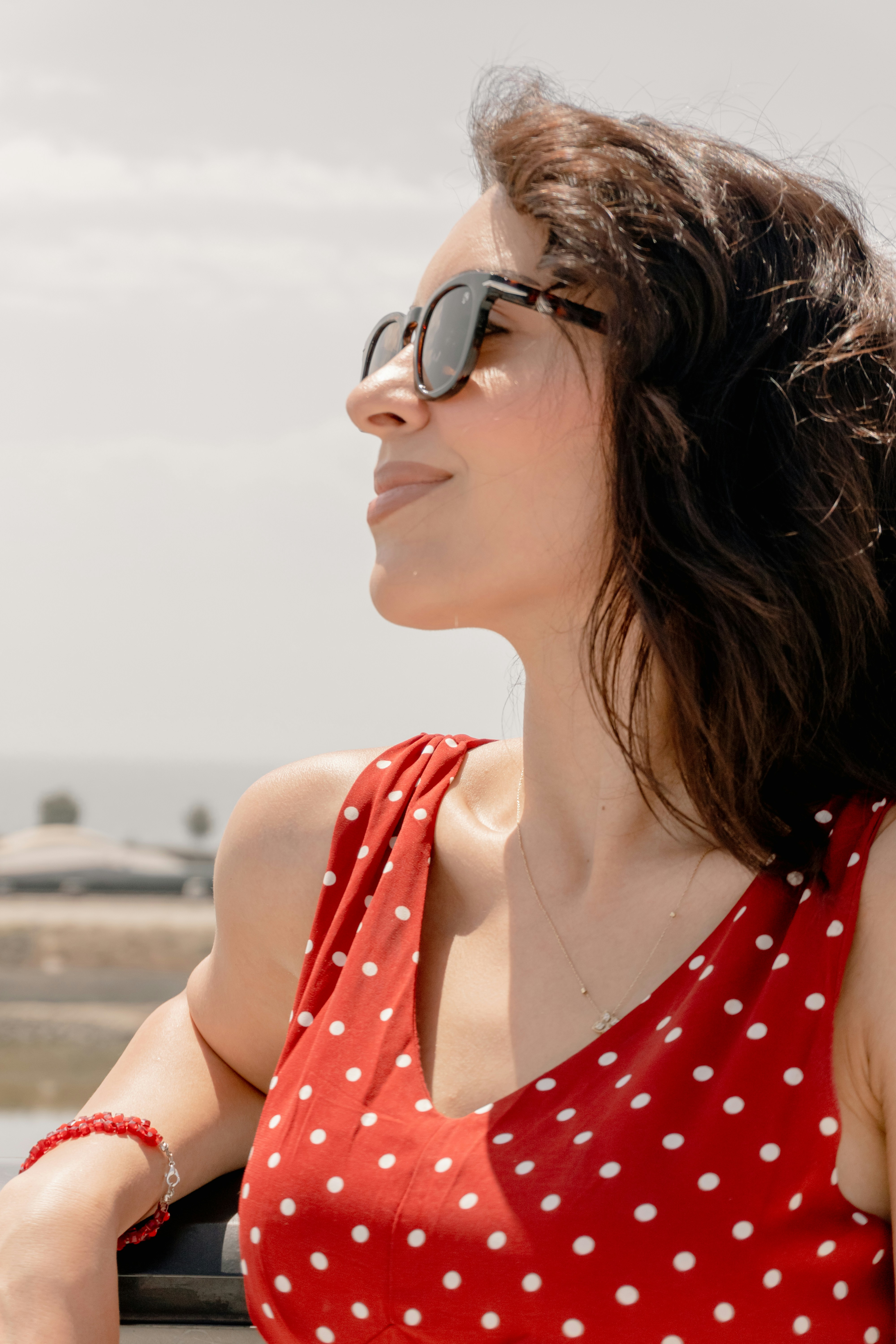 A woman in a red polka dot dress and sunglasses outdoors in bright light