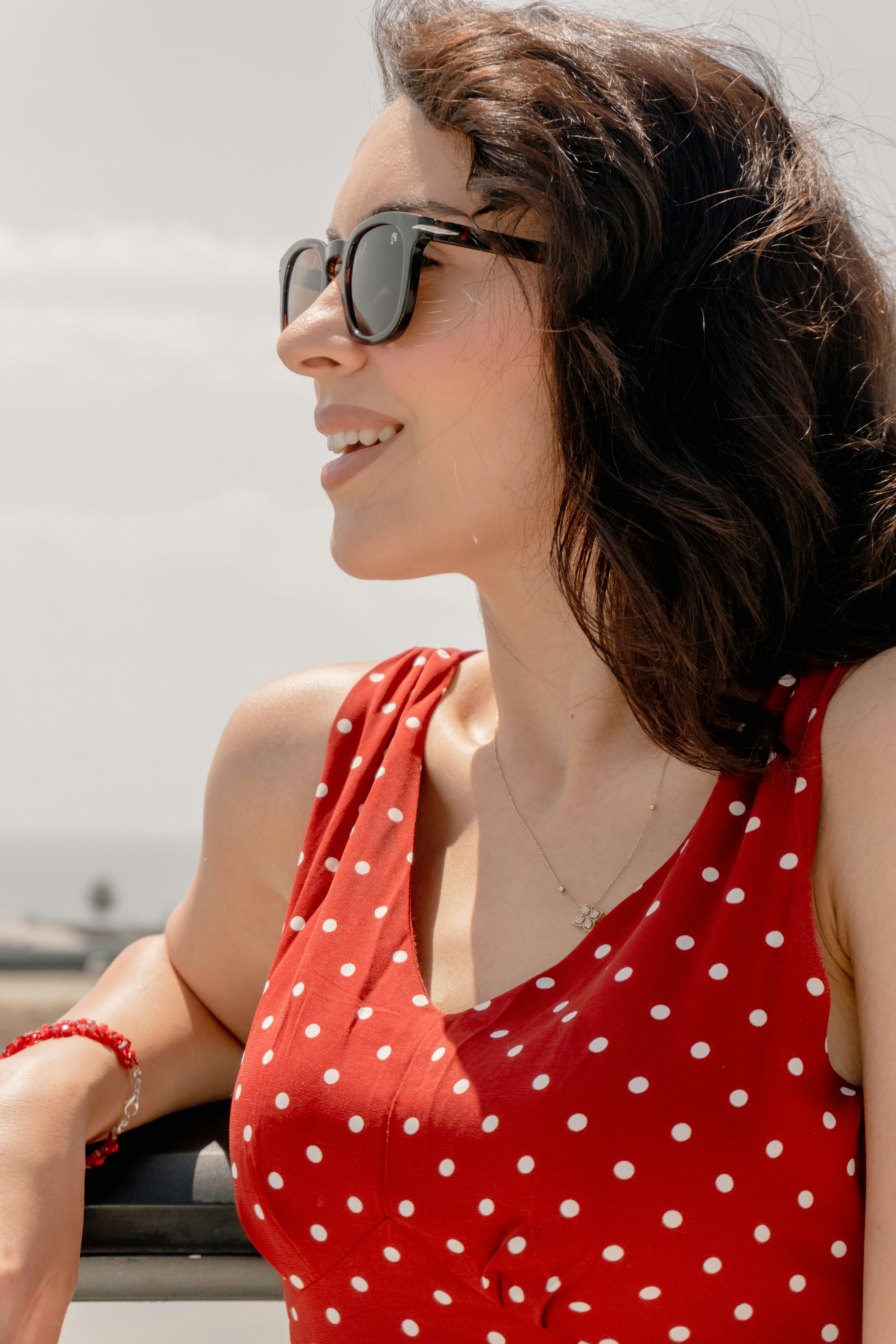 A woman in a red polka dot dress wearing sunglasses and a gold necklace