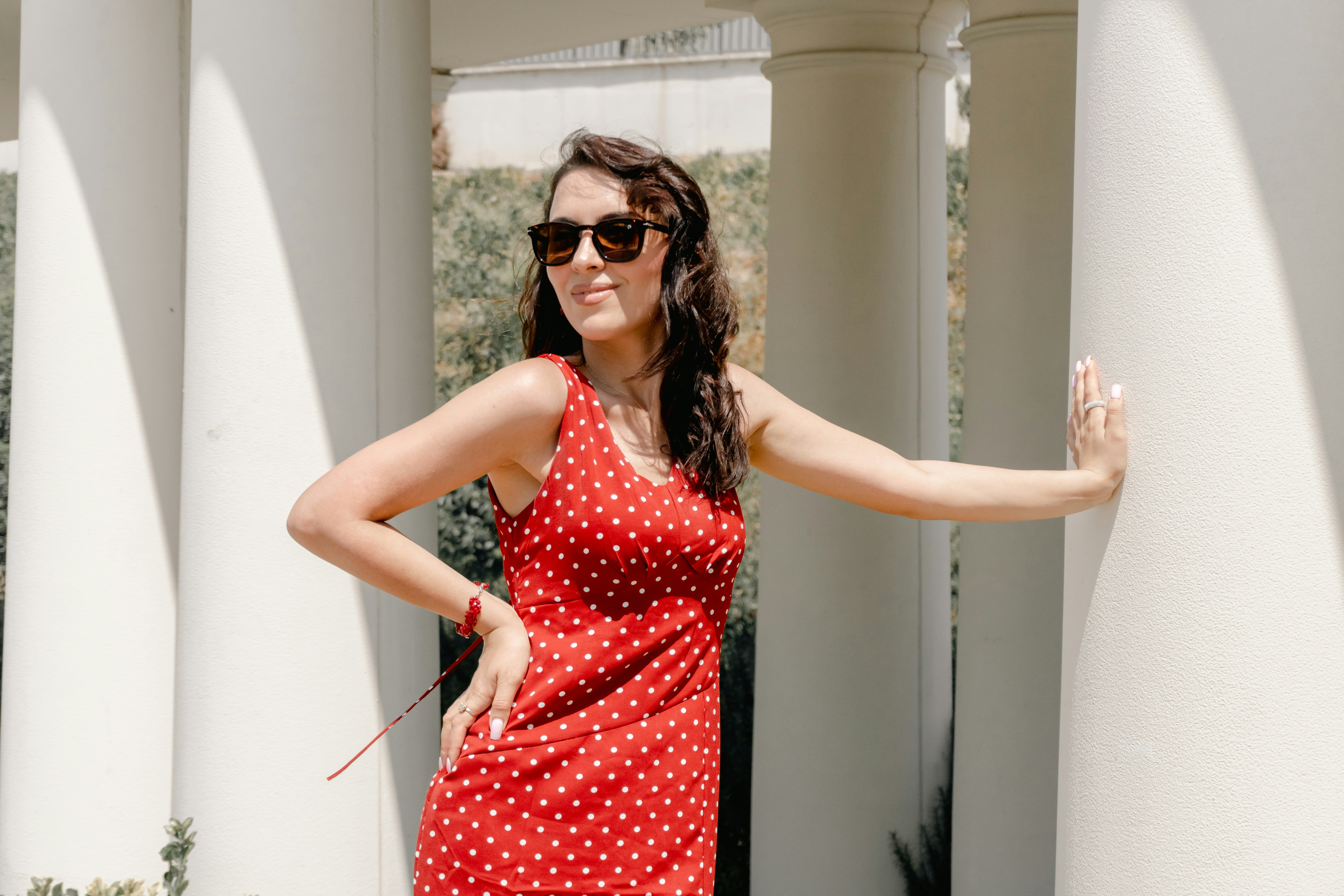 A woman in a red polka dot dress leaning against a white pillar