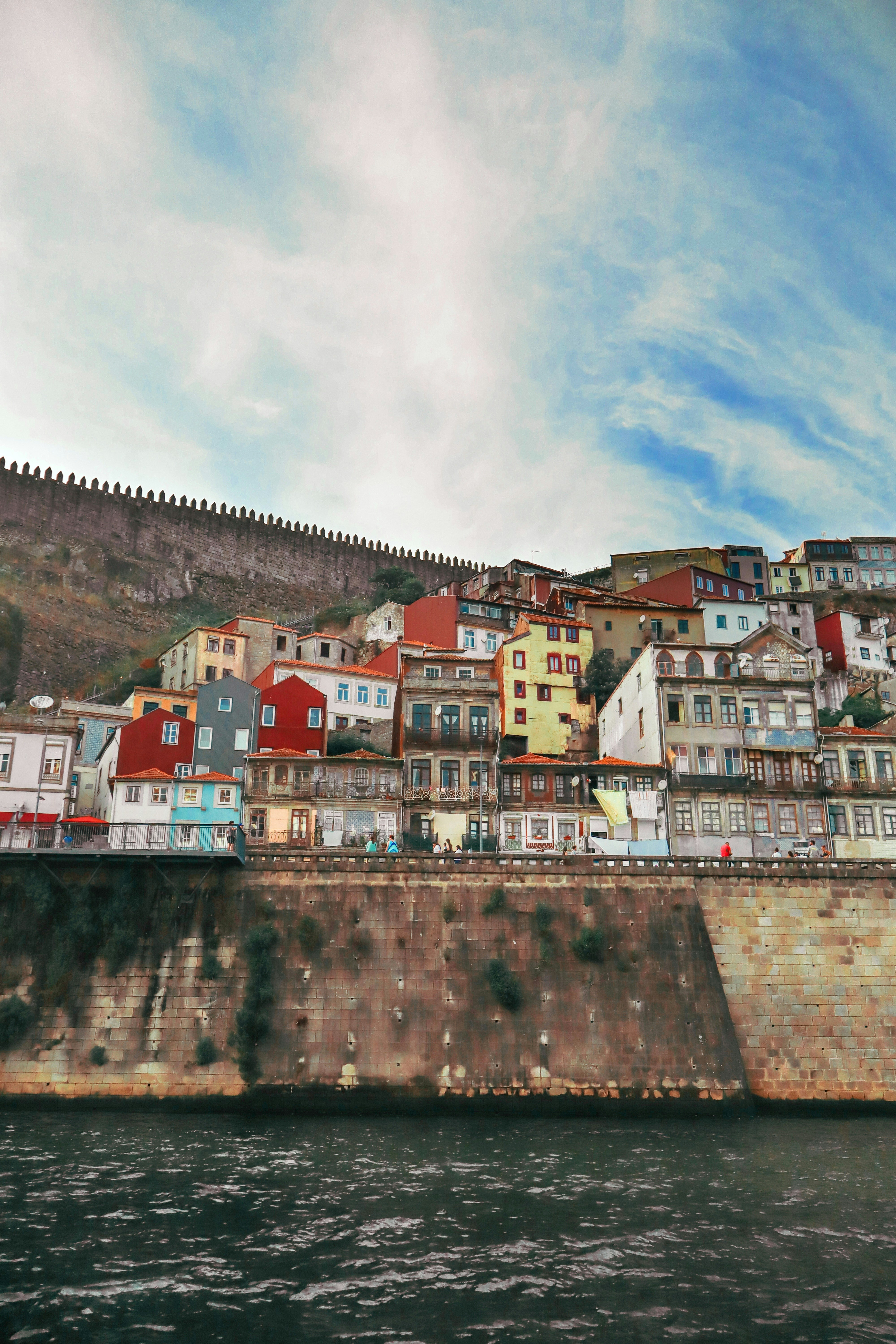 Colorful hillside houses cling to a sunlit seawall under a sweeping sky