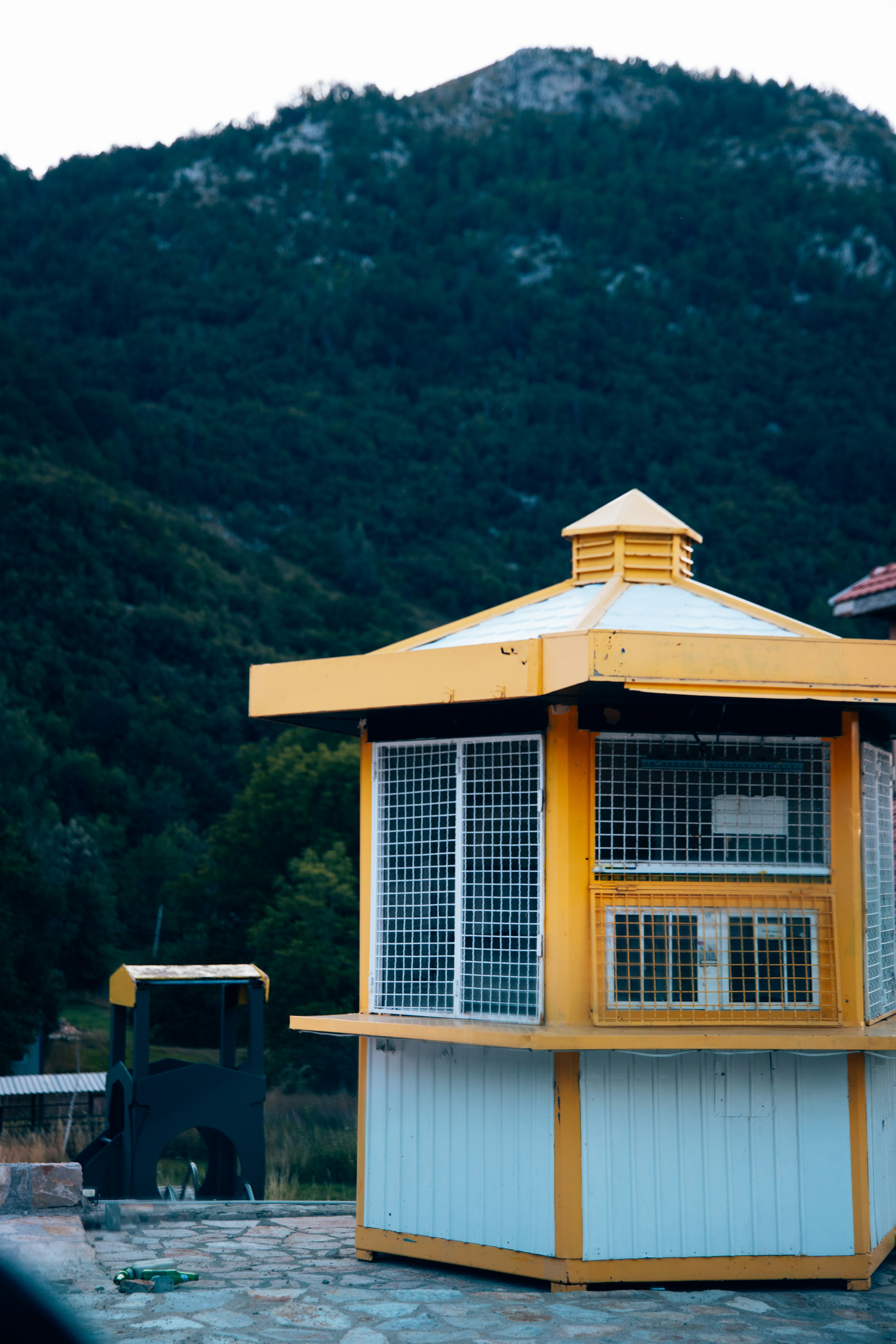 Yellow kiosk at the edge of a stone plaza with forested hills in the background