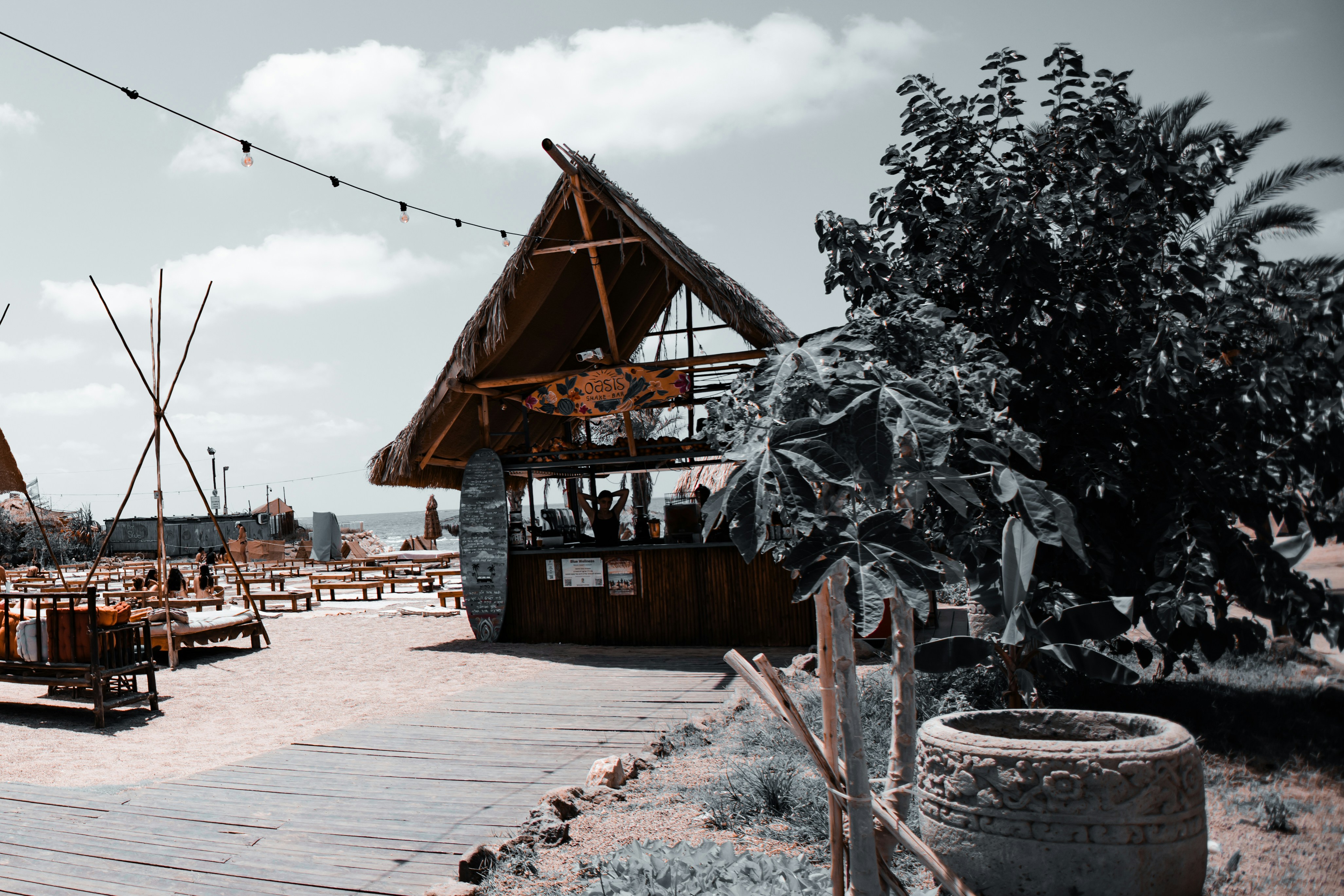 A thatched roof beach bar with a wooden boardwalk and lounge chairs