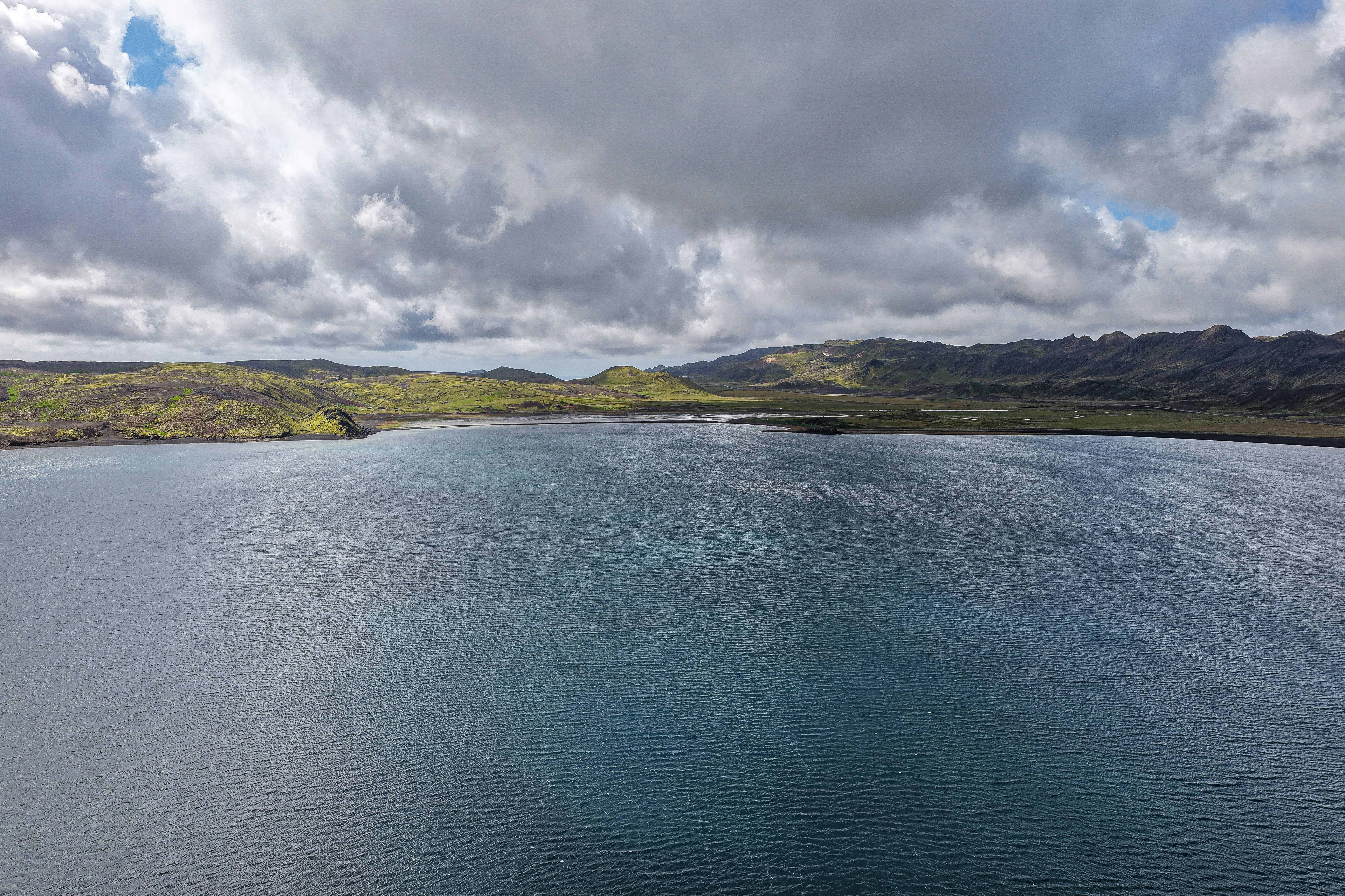 Expanse of Glassy Water Meeting Distant Moorland under Clouded Sky