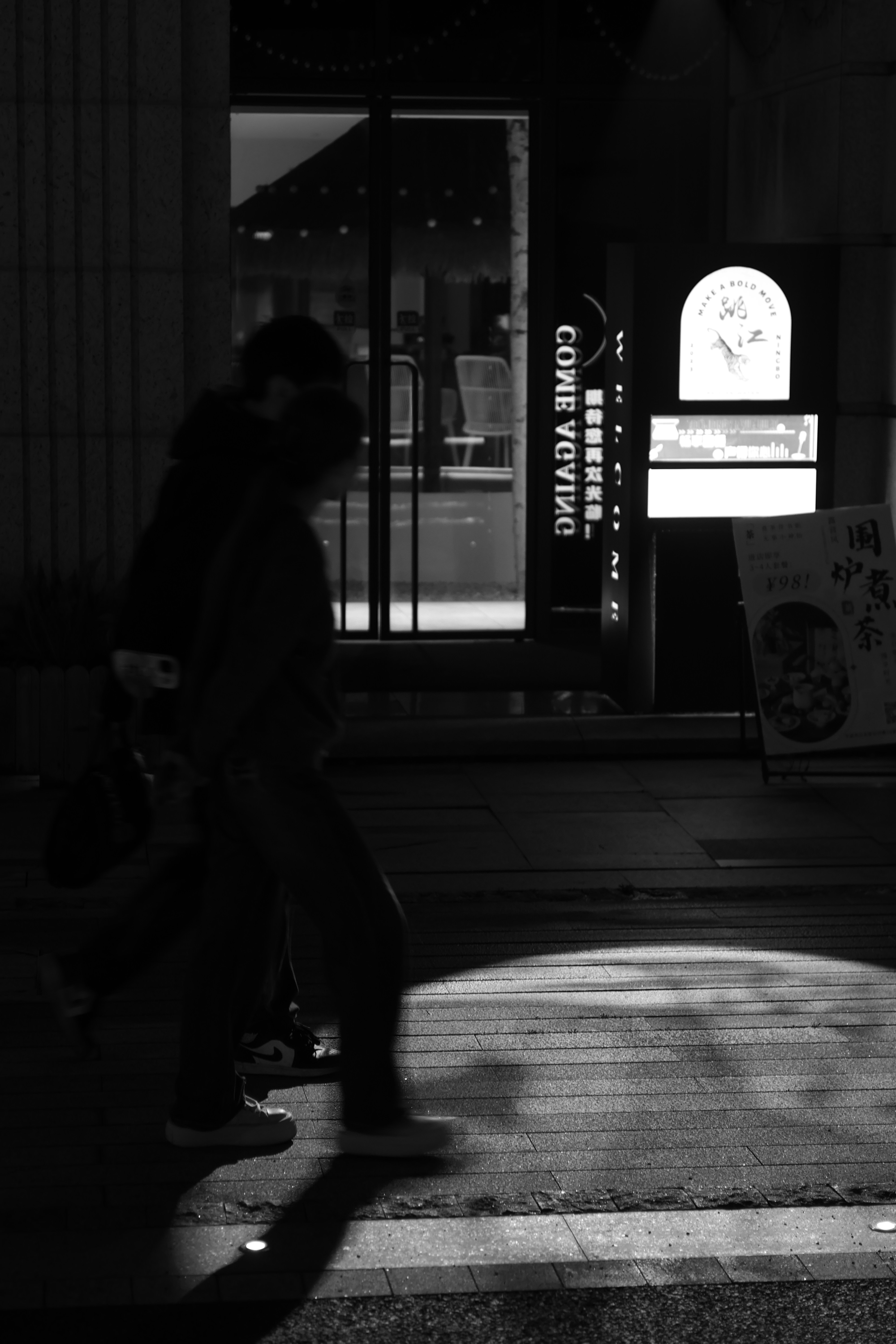 Shadowed Pedestrians Exit into Light by a Neon Gate