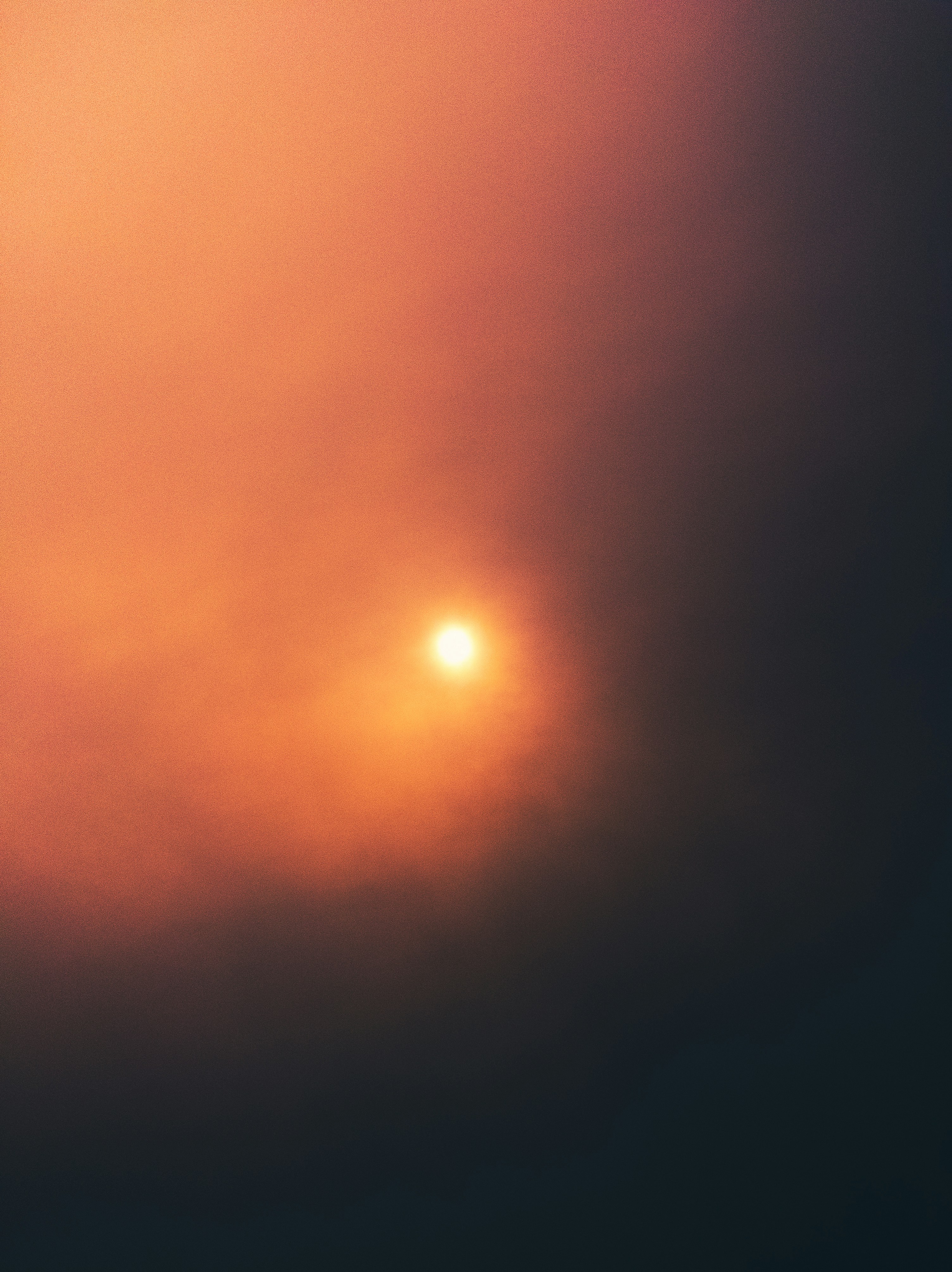Warm sun through hazy clouds with a soft orange glow fading into dark blue, a minimal abstract scene.