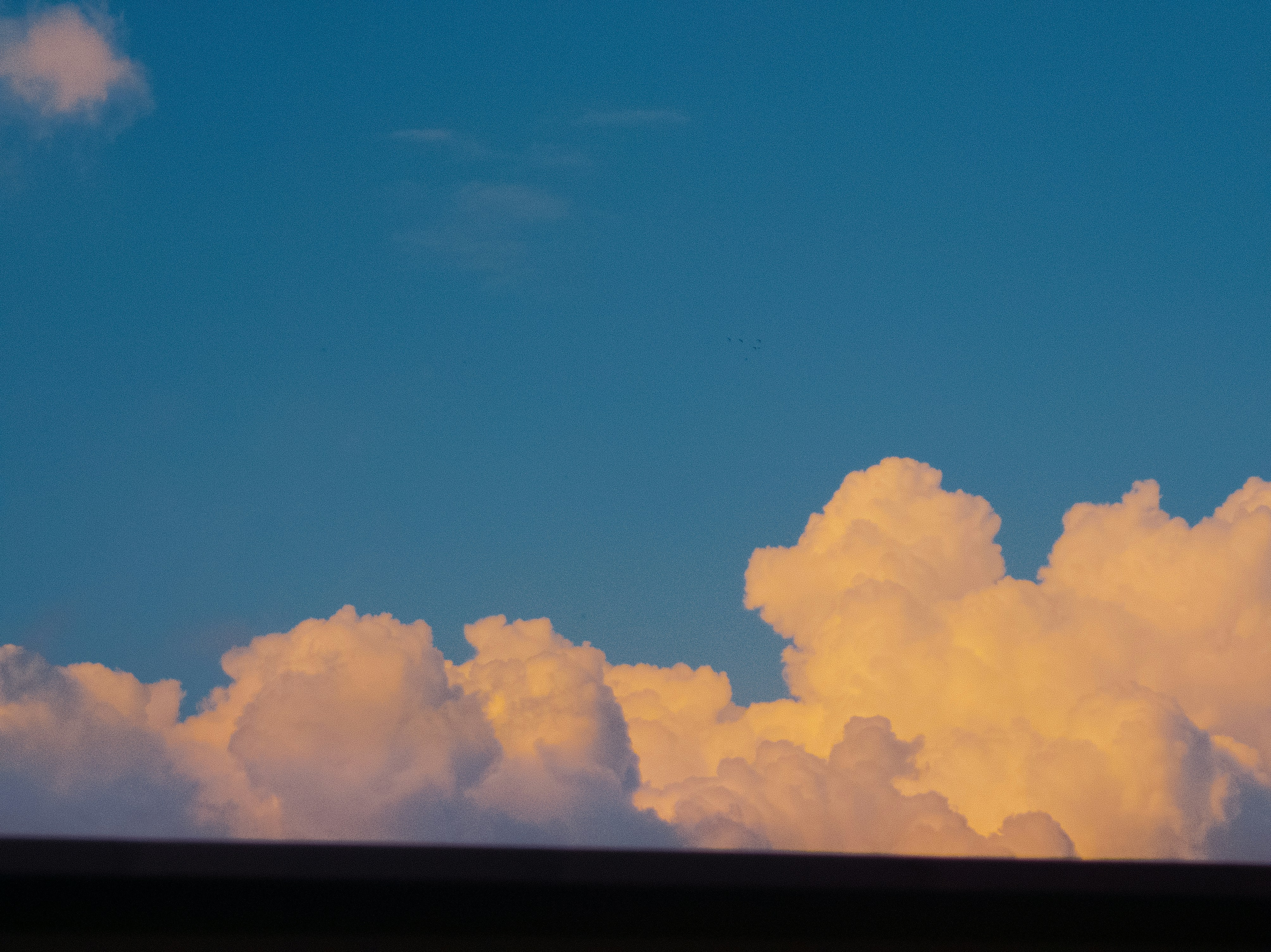 Quiet Horizon: Blue Sky and Golden Clouds above a Dark Silhouette