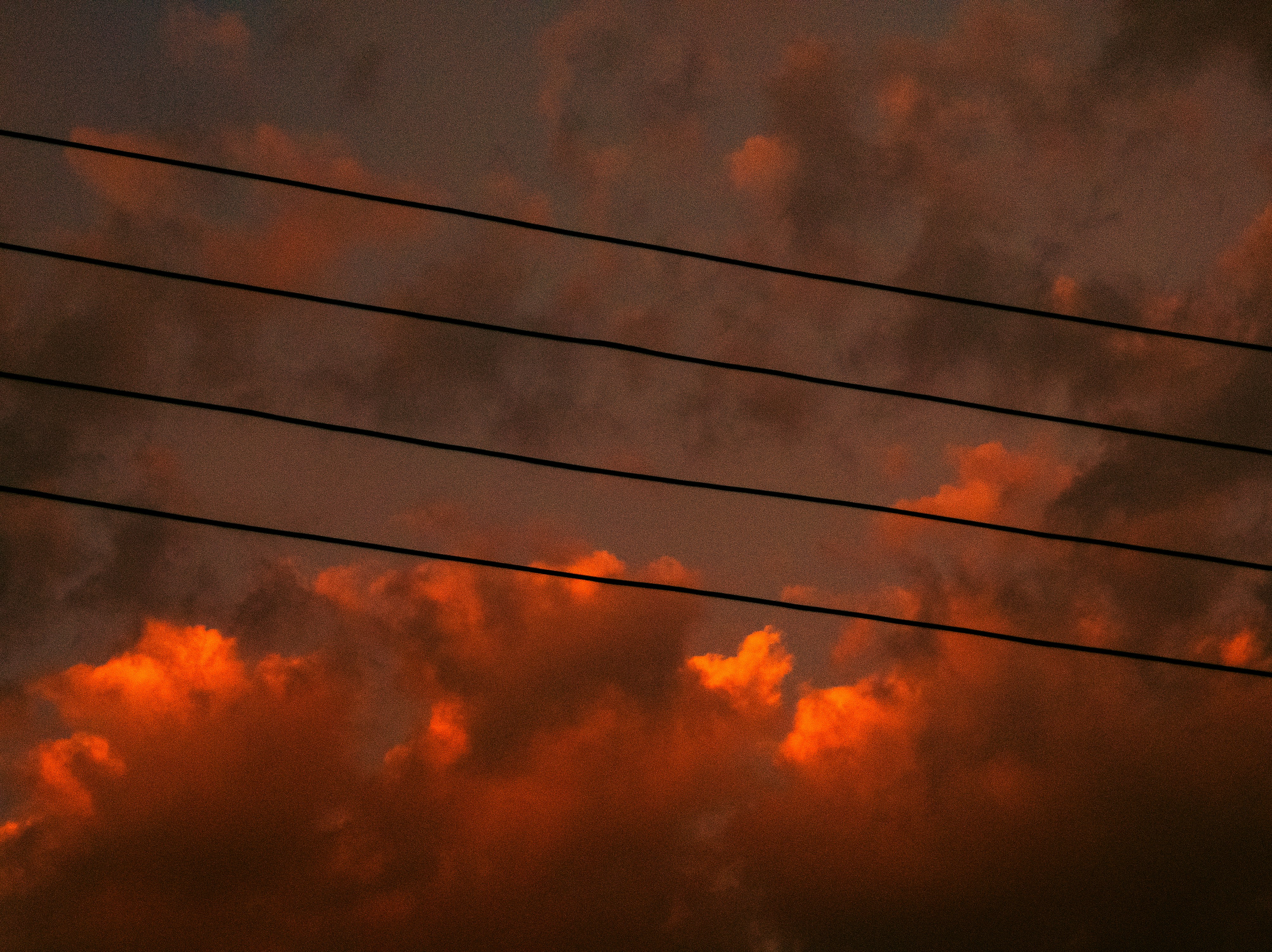 Juxtaposed orange clouds glow beneath a darkened sky, with diagonal power lines cutting across the frame.