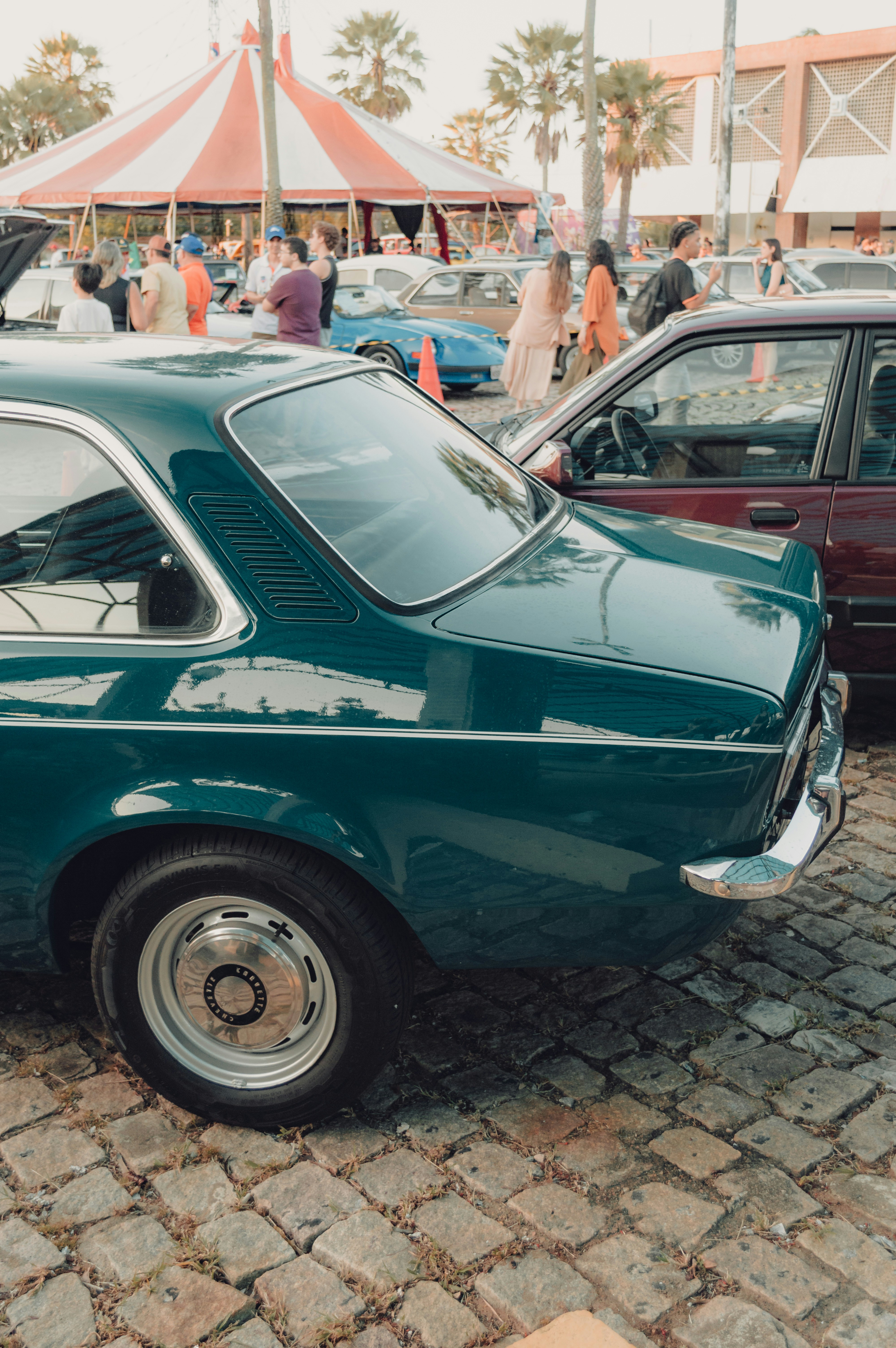 A teal vintage coupe with cobblestone charm at a sunlit festival