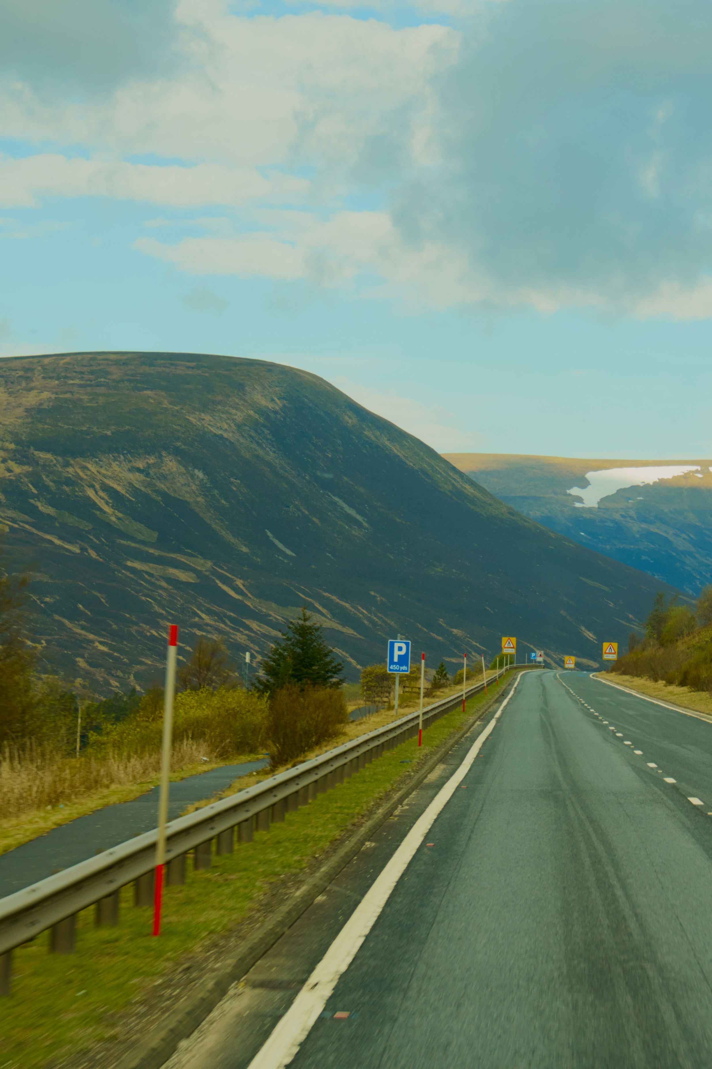 Deserted highway winds toward distant mountains under a soft blue sky; the landscape emphasizes depth and scale with roadside signs guiding the way. This is a photographic landscape.