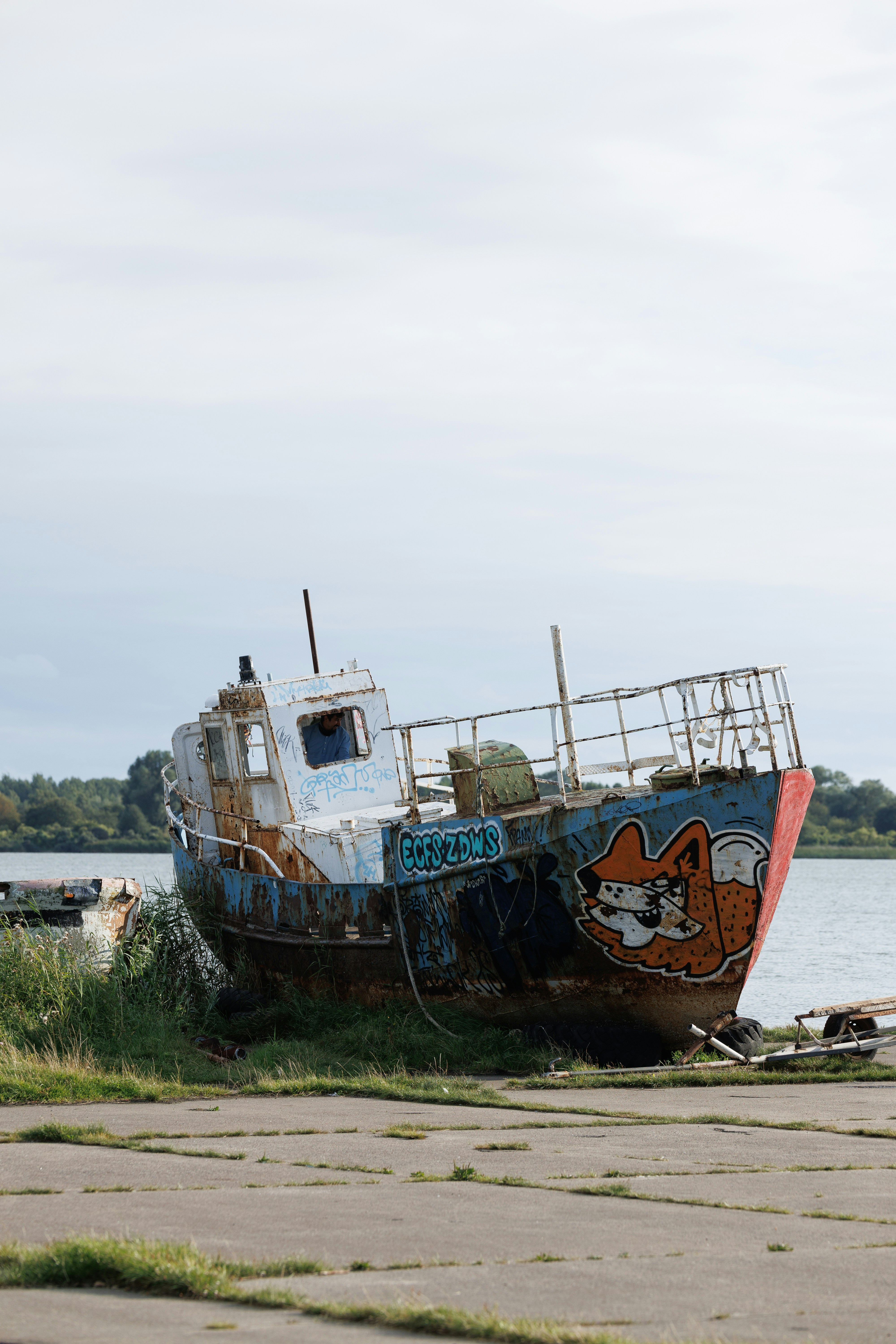 Painted Vessel at the Water’s Edge: A Rusted Barge with Graffiti Under A Quiet Sky