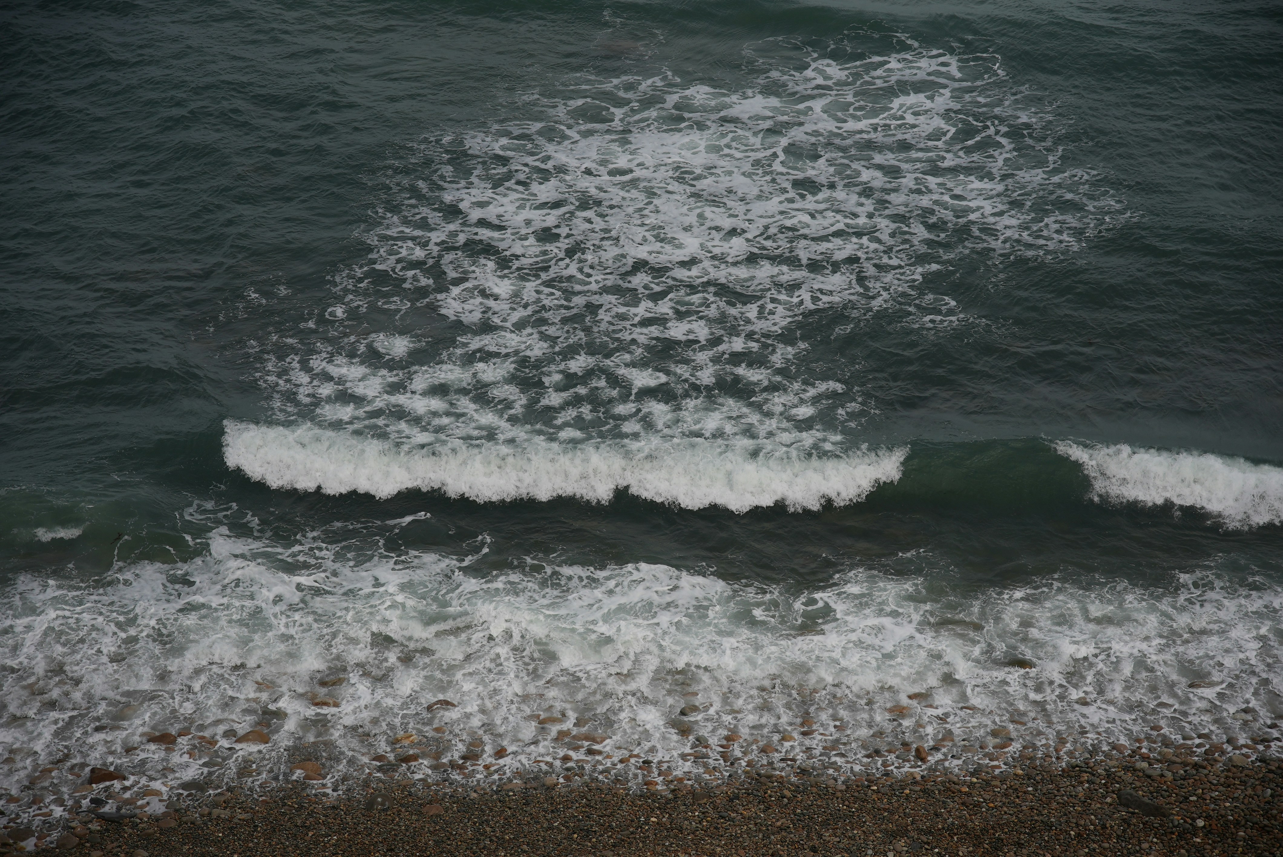 Foamy shoreline choreography: waves meet pebbled beach