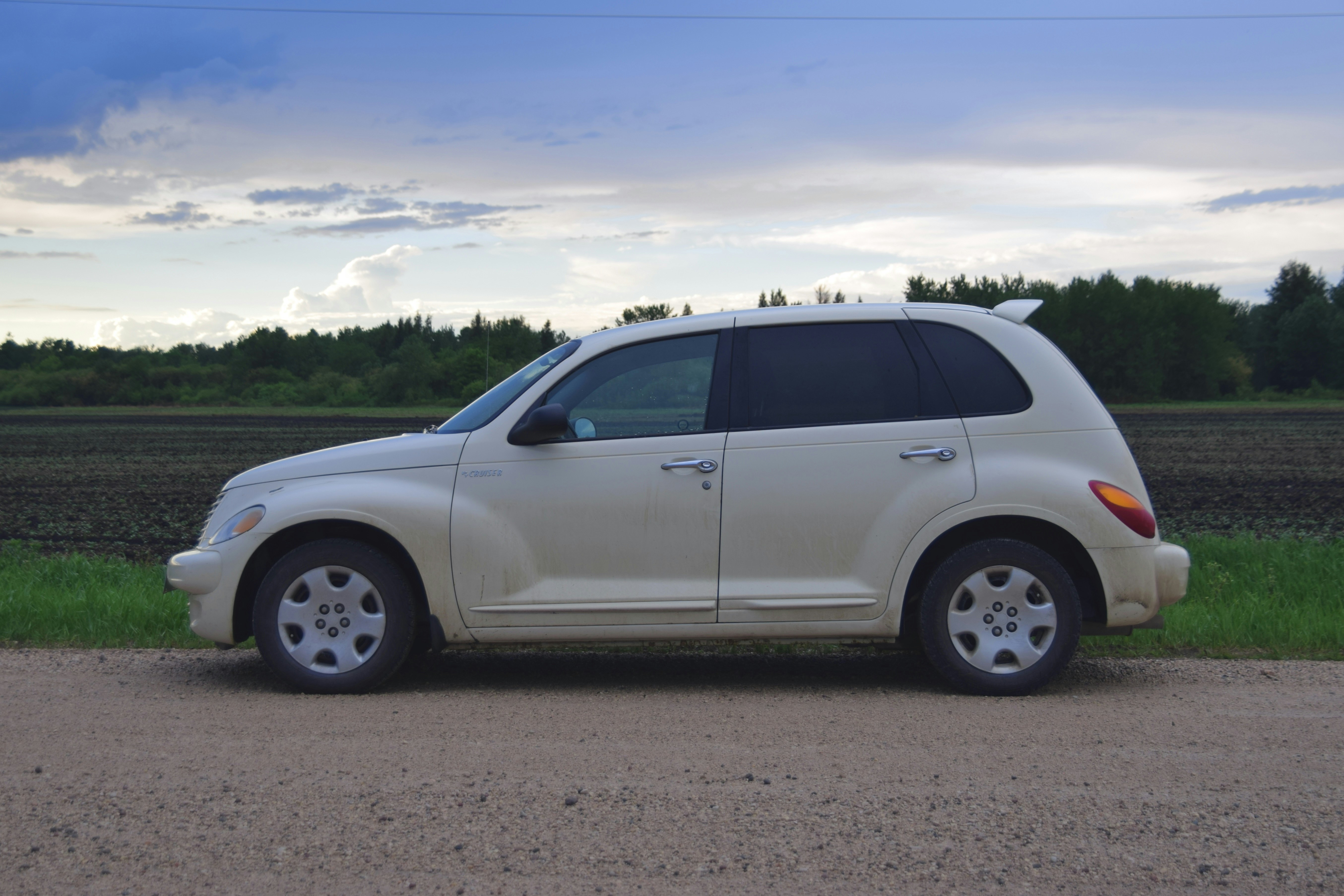 White SUV resting on a rural road with fields and trees beneath a cloudy sky