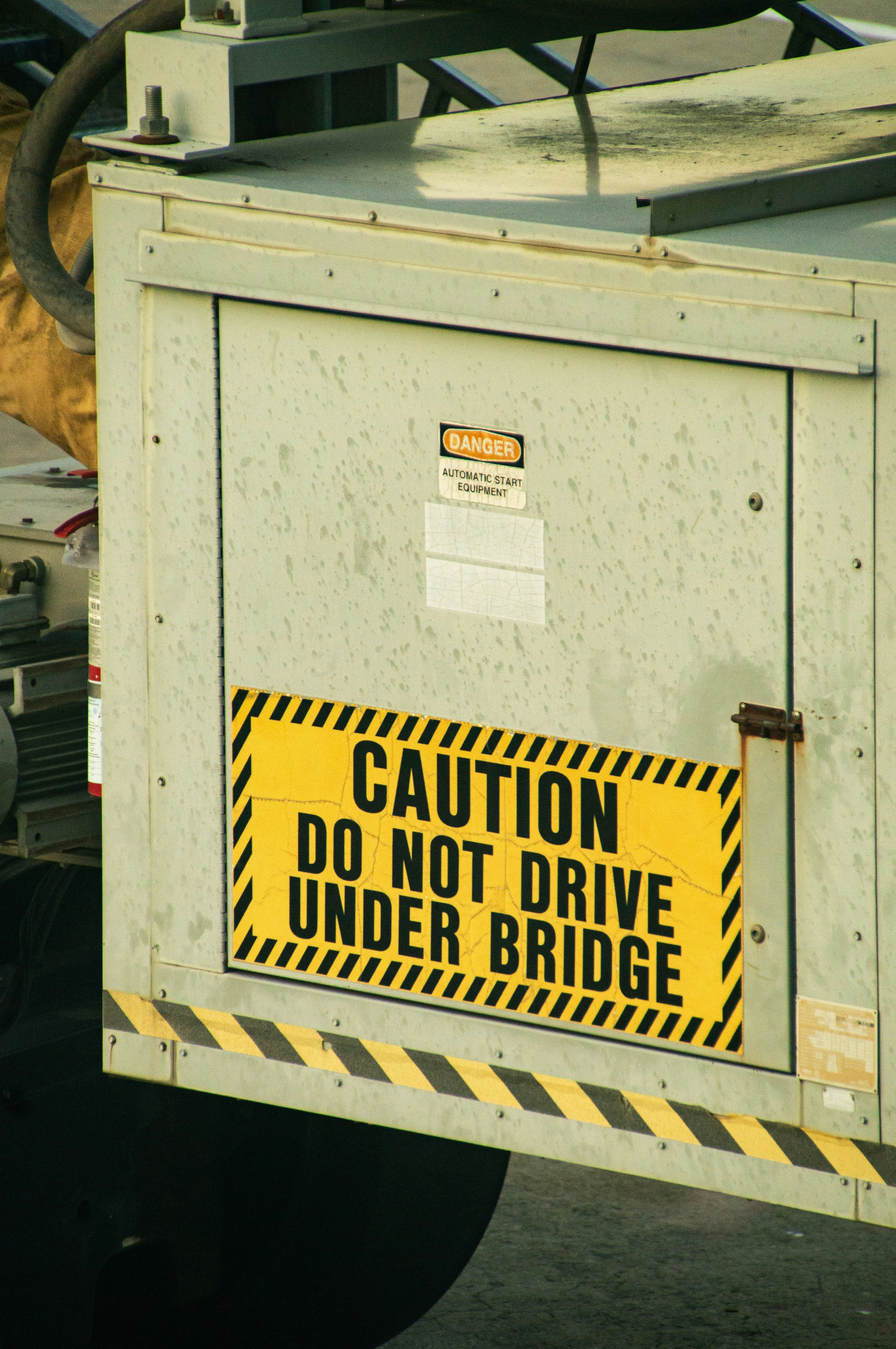 A yellow caution sign reading DO NOT DRIVE UNDER BRIDGE on industrial equipment