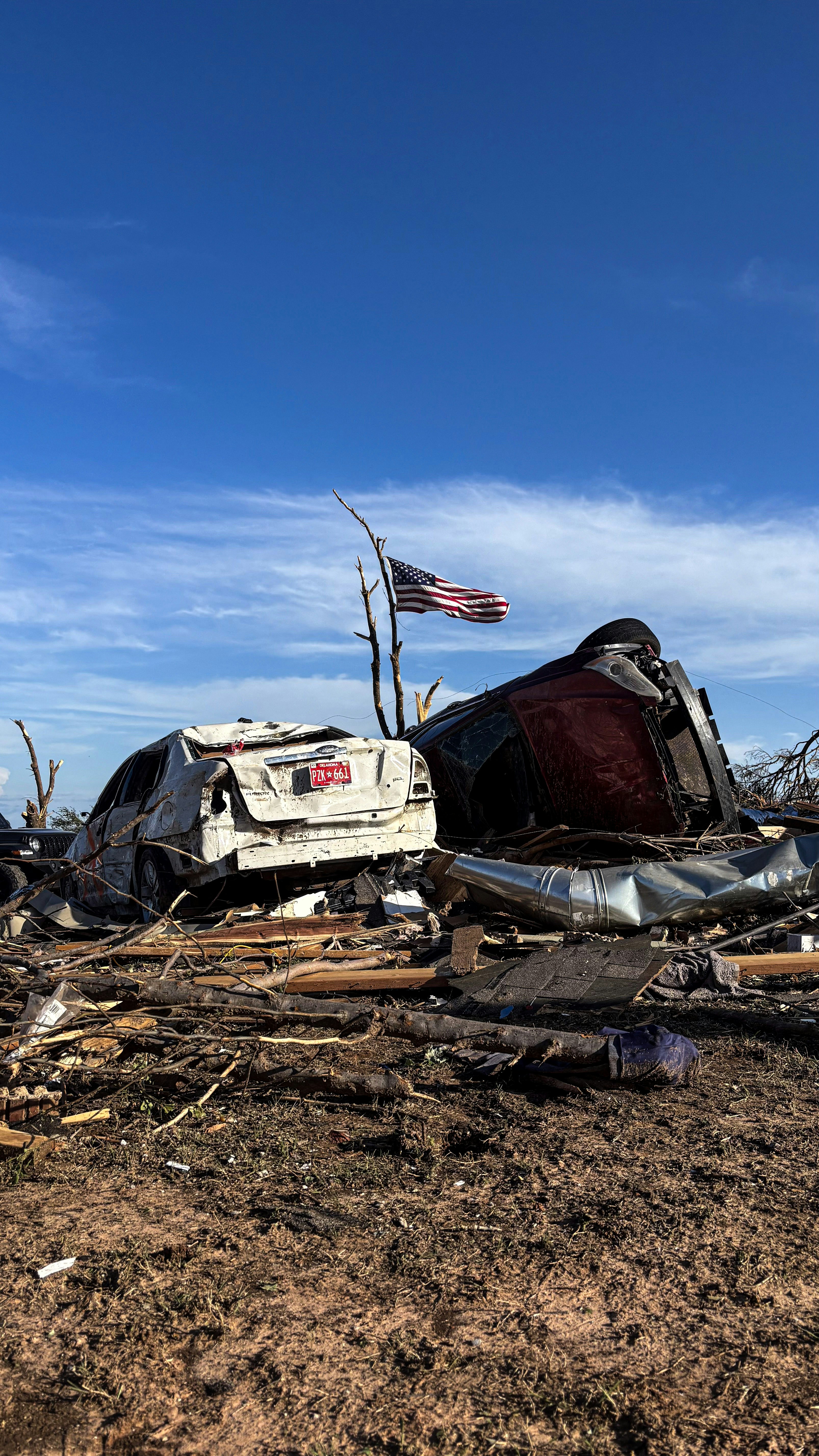 Flag Above the Wreckage: aftermath under a wide blue sky
