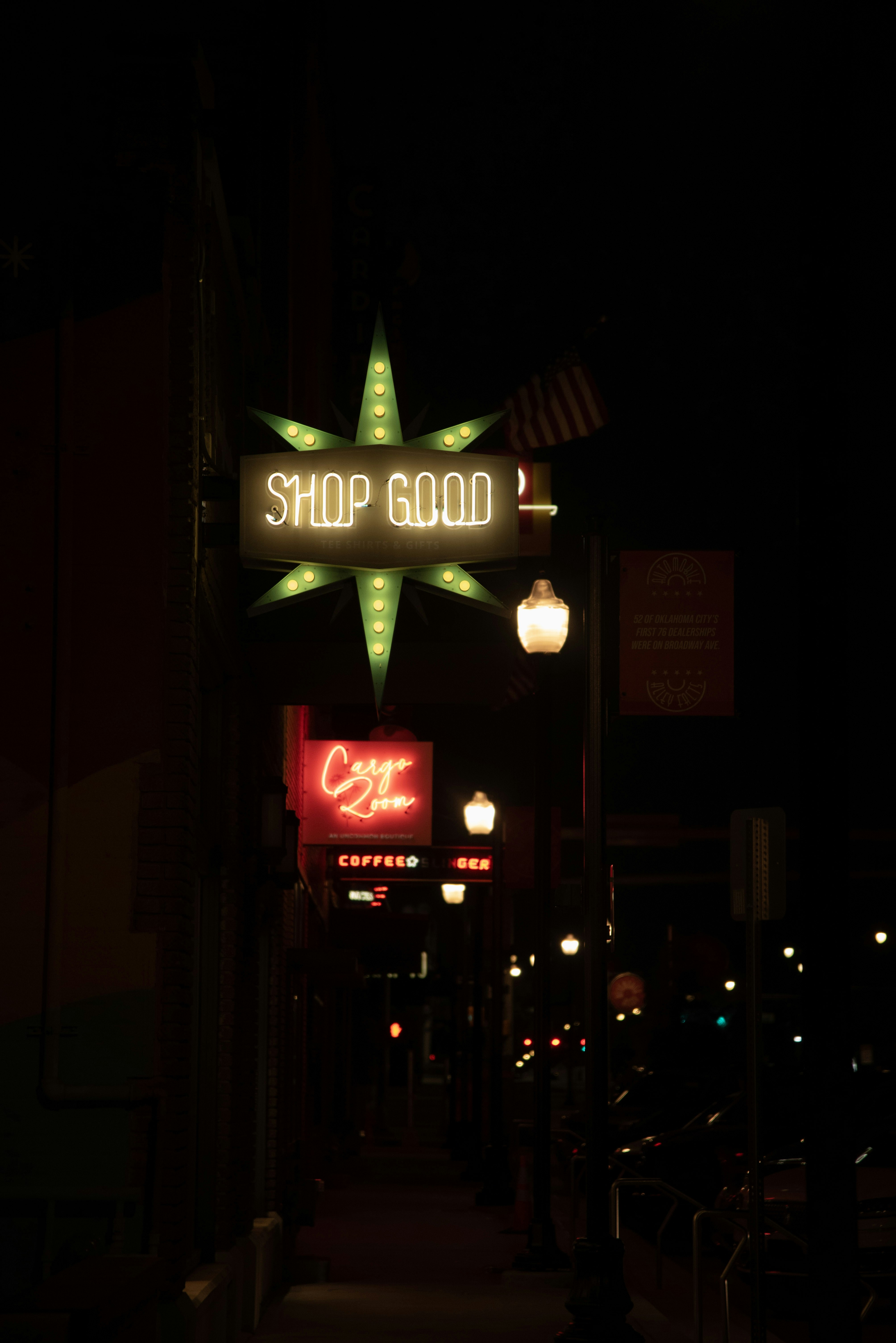 A star-shaped neon sign reading SHOP GOOD above a dark city sidewalk at night