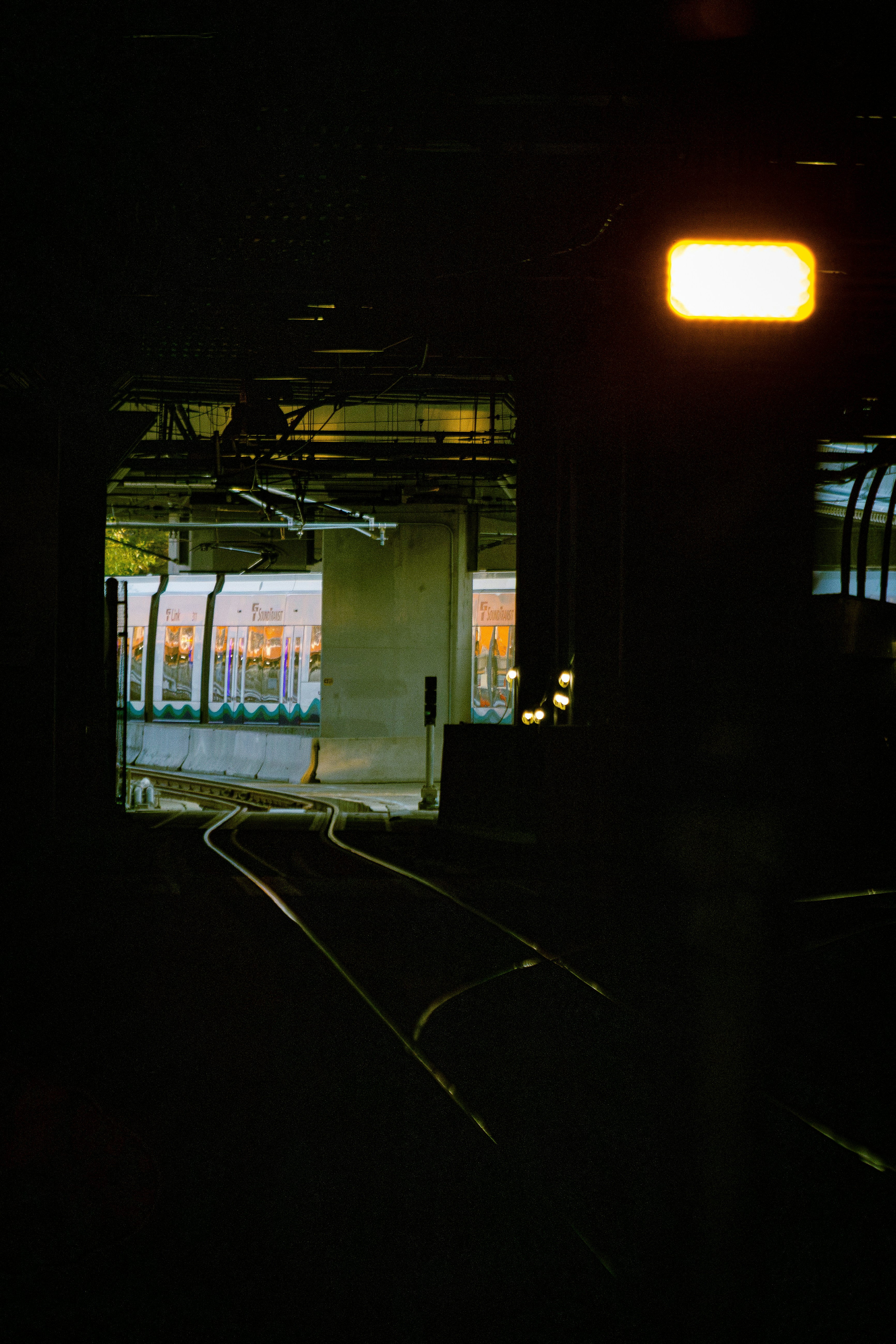 A light rail train passing through a dark tunnel with a glowing yellow signal