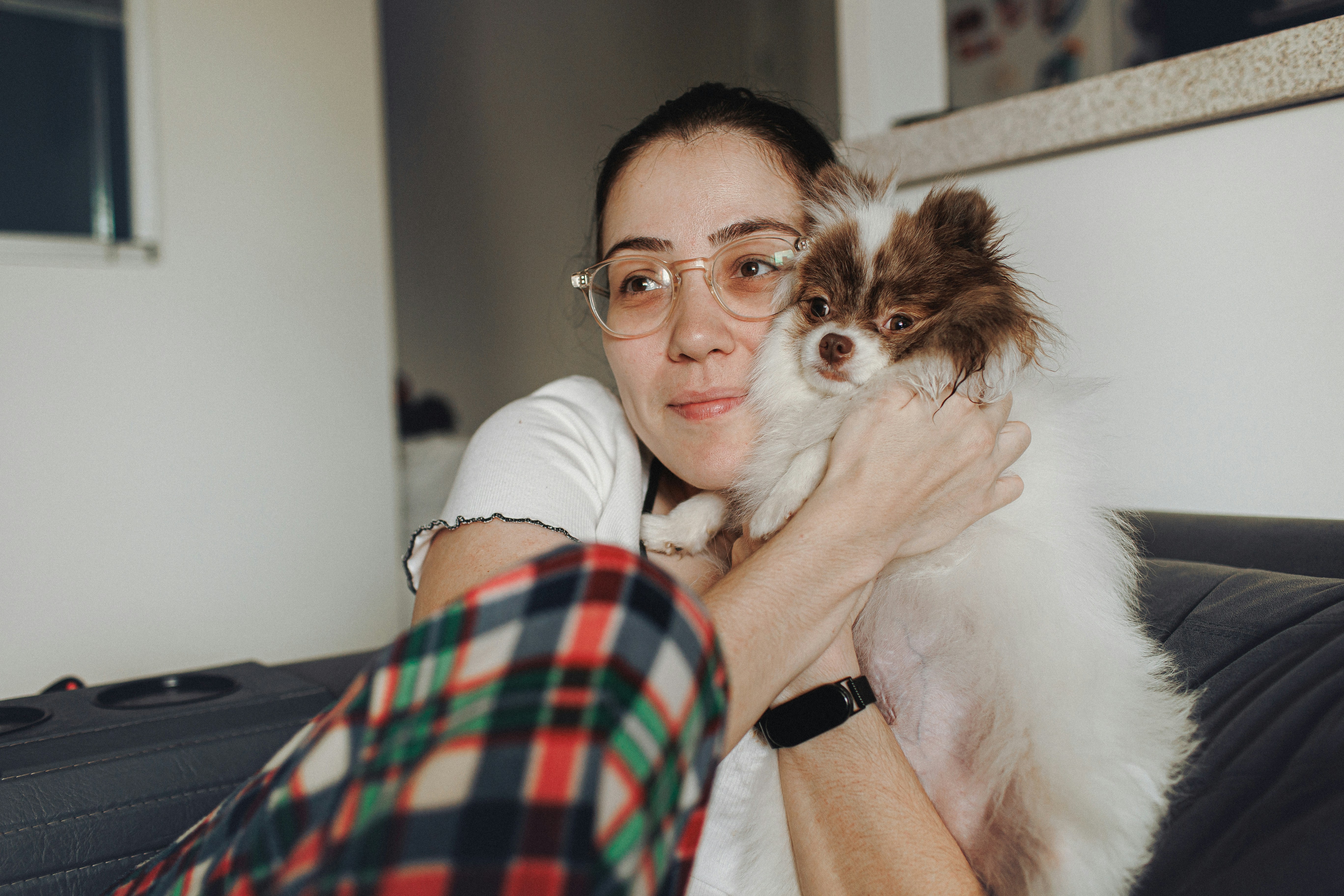 A woman cradles a small fluffy dog close to her face on a couch, capturing a warm, intimate moment.