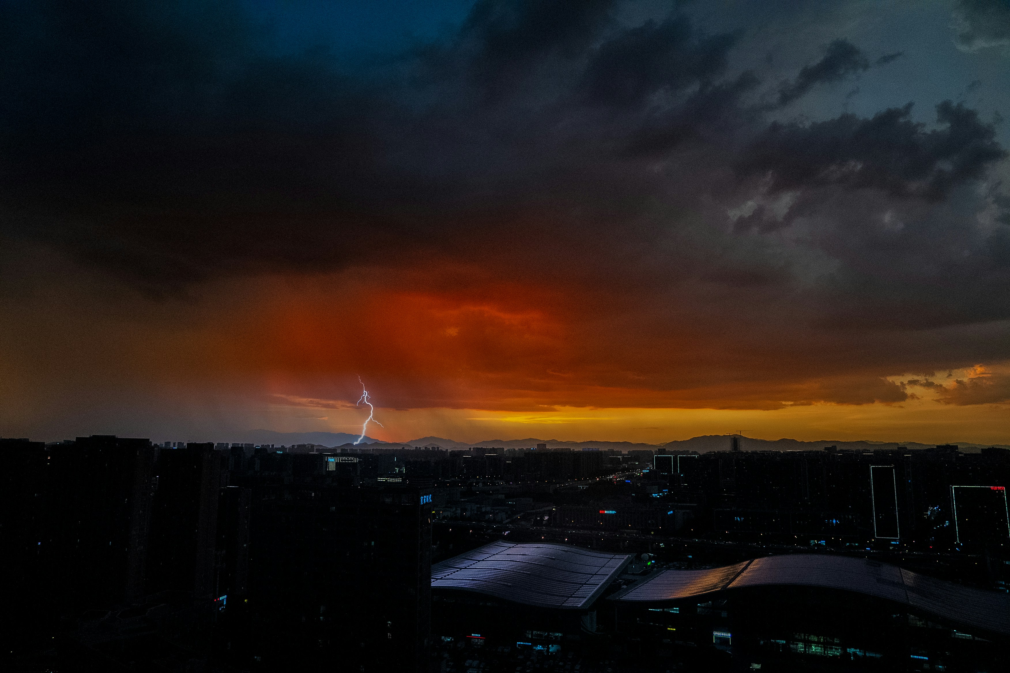 A lightning bolt striking over a dark city skyline under a glowing orange sky