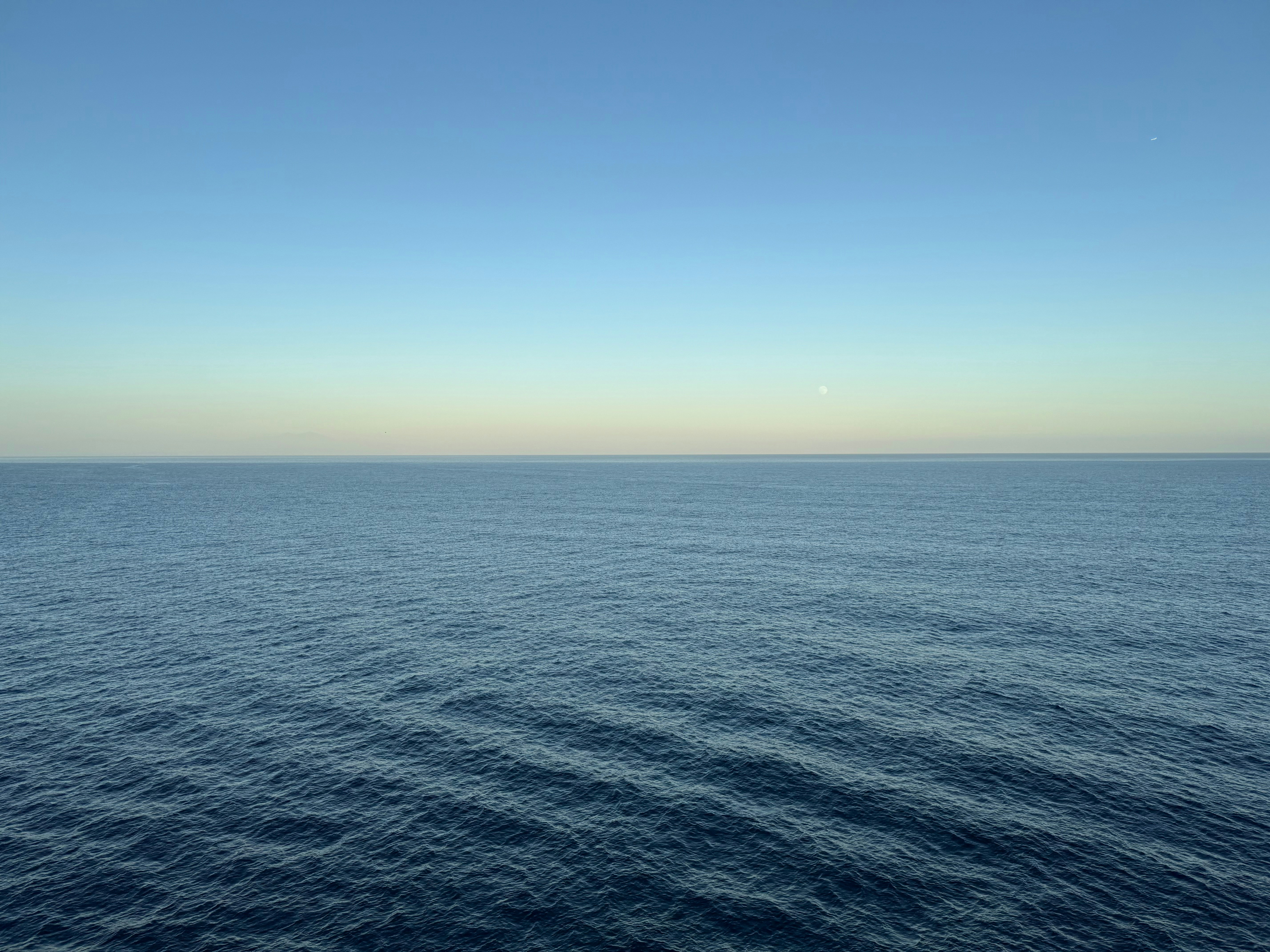 Expansive ocean under a gradient sky with a distant horizon, emphasizing calm water texture. (Still image).