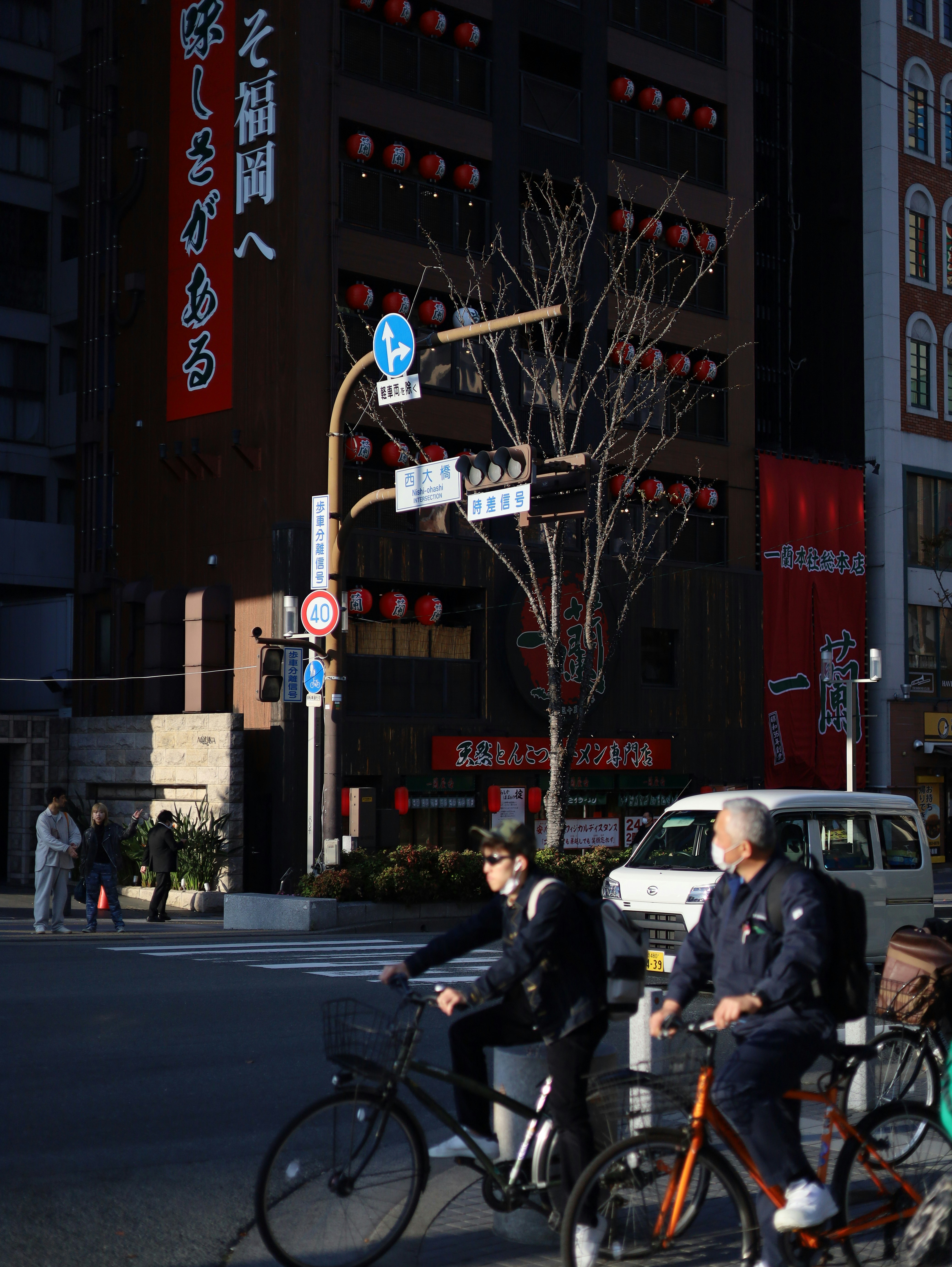 Busy city street with cyclists in the foreground and a building adorned with red lanterns in the background, emphasizing urban life and motion.