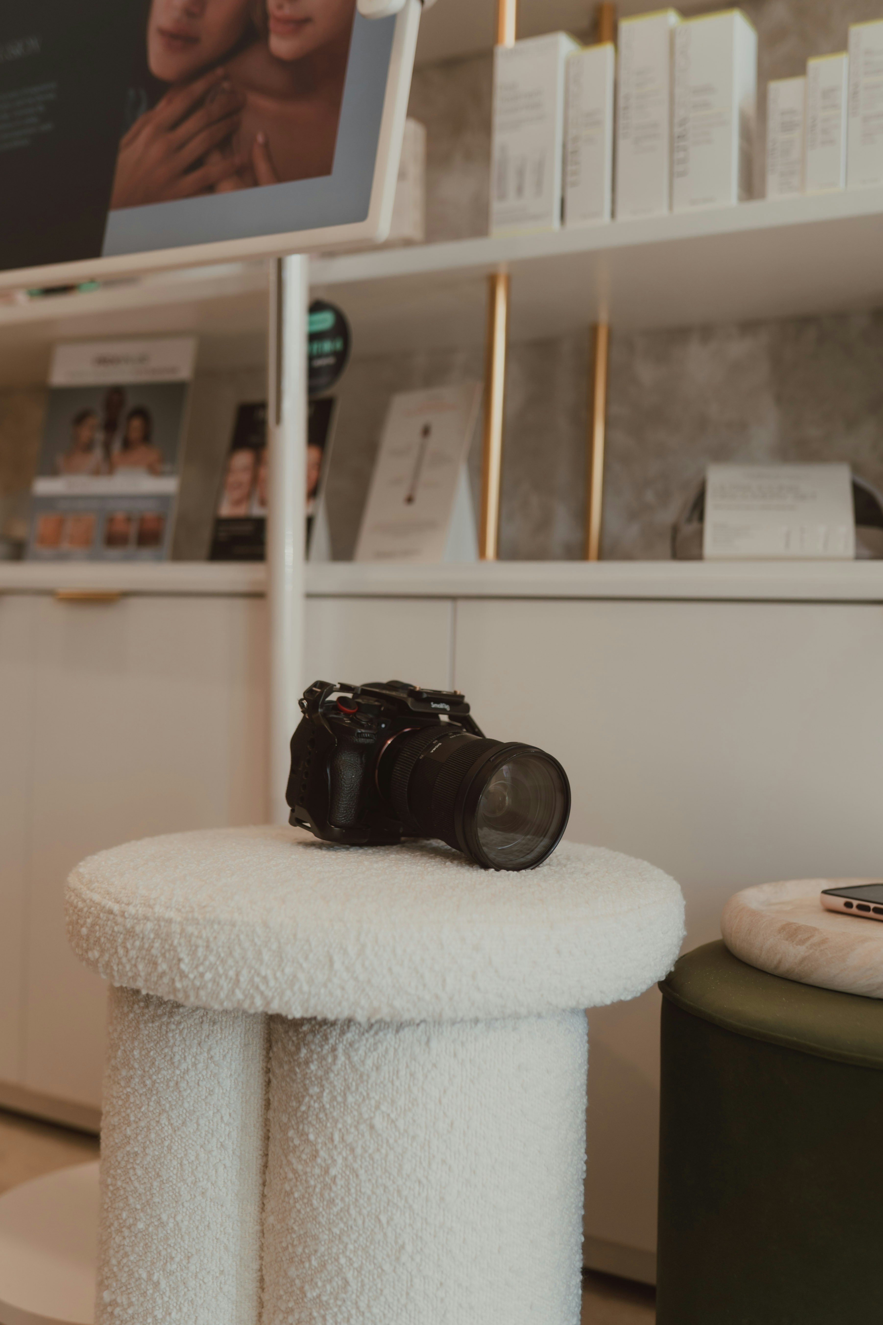 A Sony mirrorless camera rests on a white textured stool in a softly lit showroom, with shelves and product displays in the blurred background.