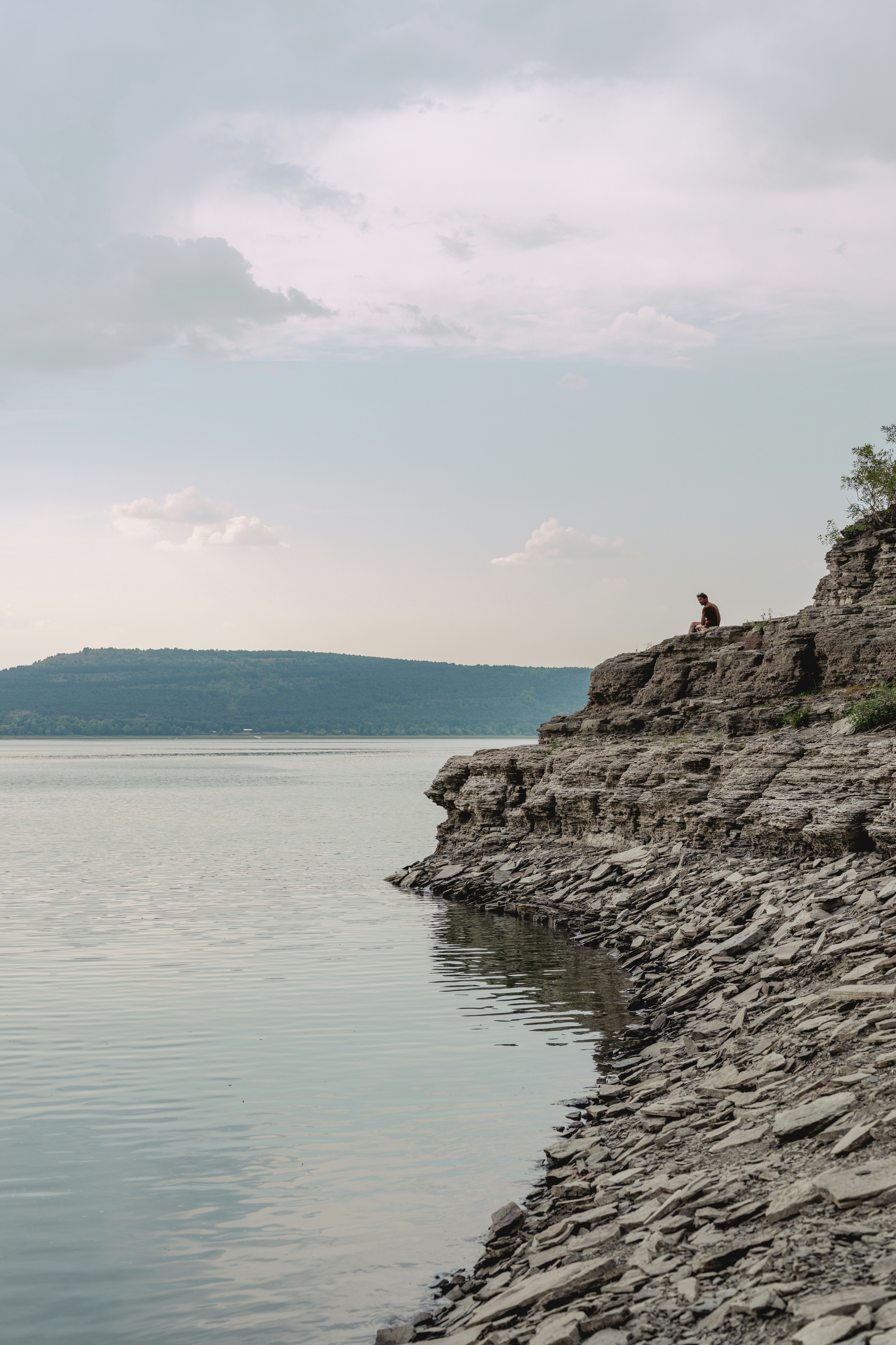 Edge of Quiet: A solitary figure on layered rock overlooking the lake