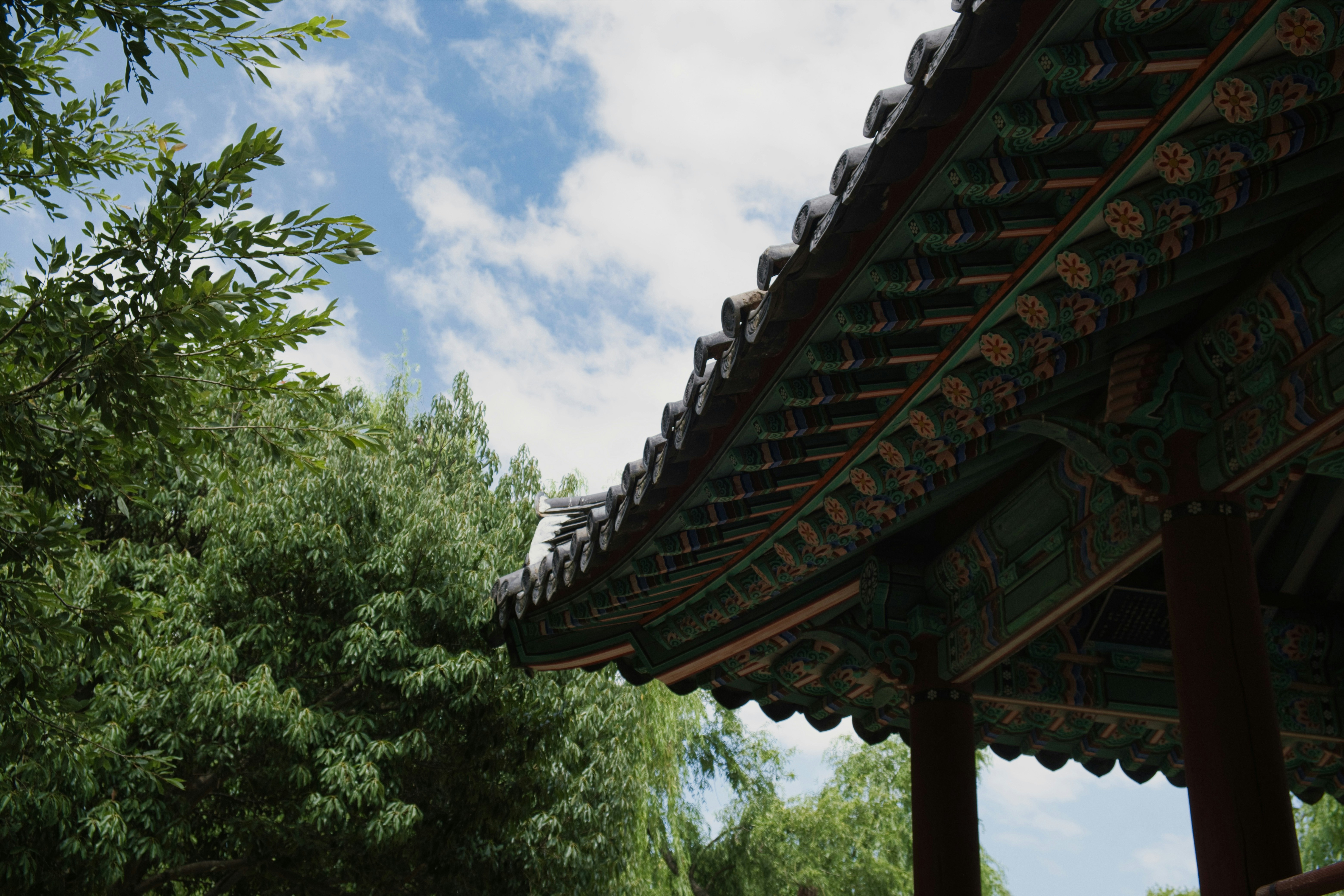 Curved eaves against a blue sky: Traditional roof lines frame a leafy courtyard