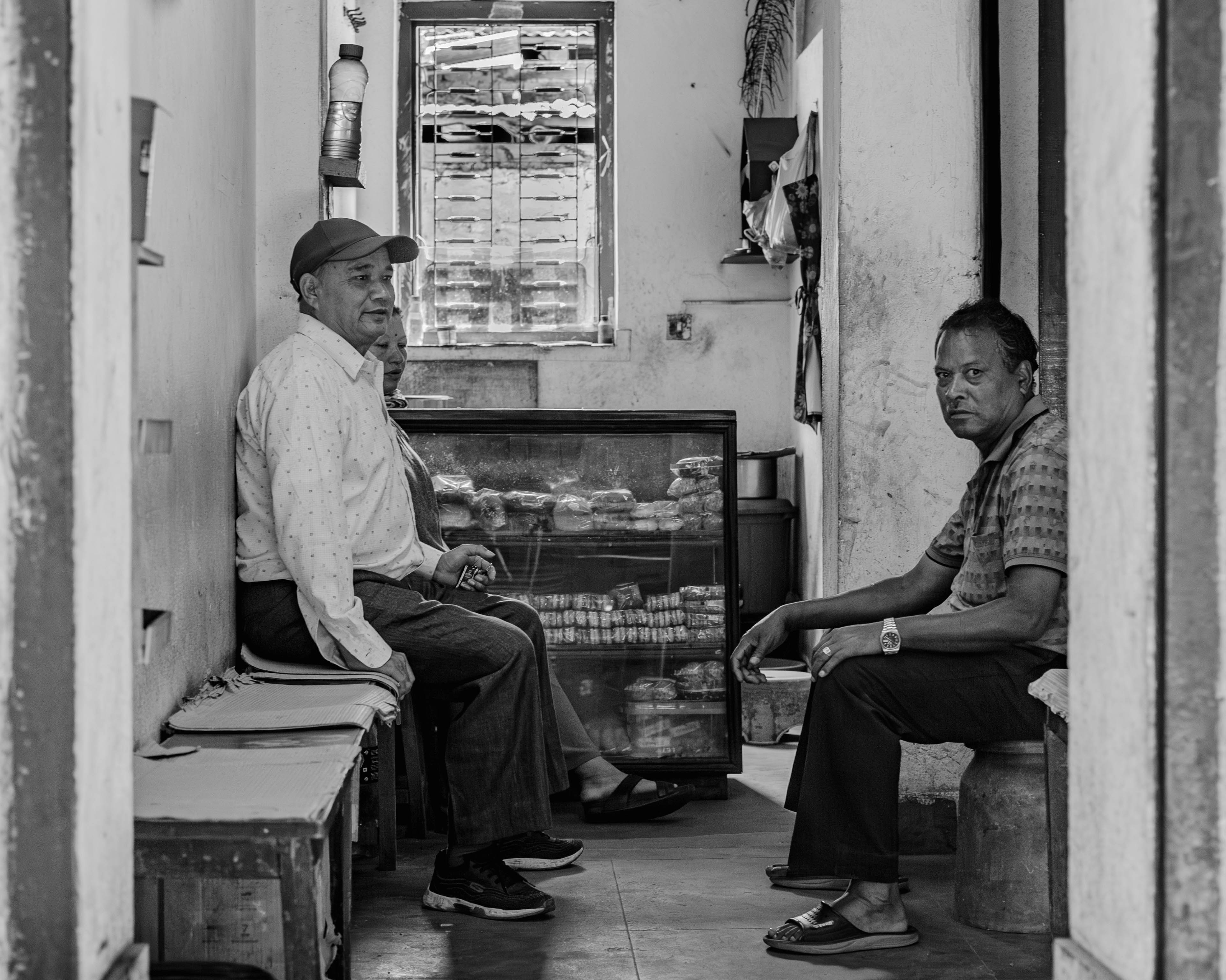 Two men sitting on benches inside a small shop with a glass display case