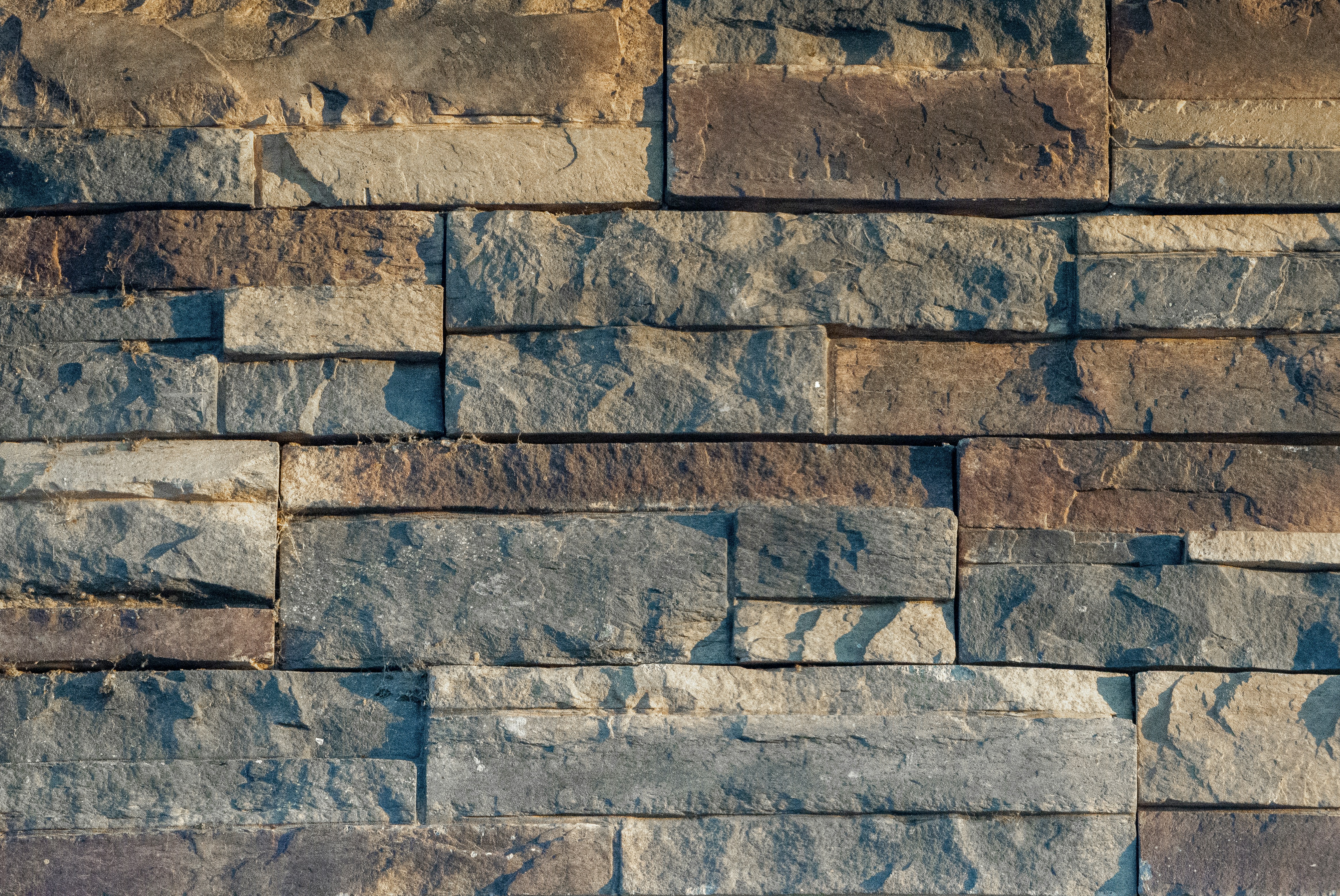 Close-up of layered stone masonry with warm sunlight and cool shadows highlighting texture and gaps.