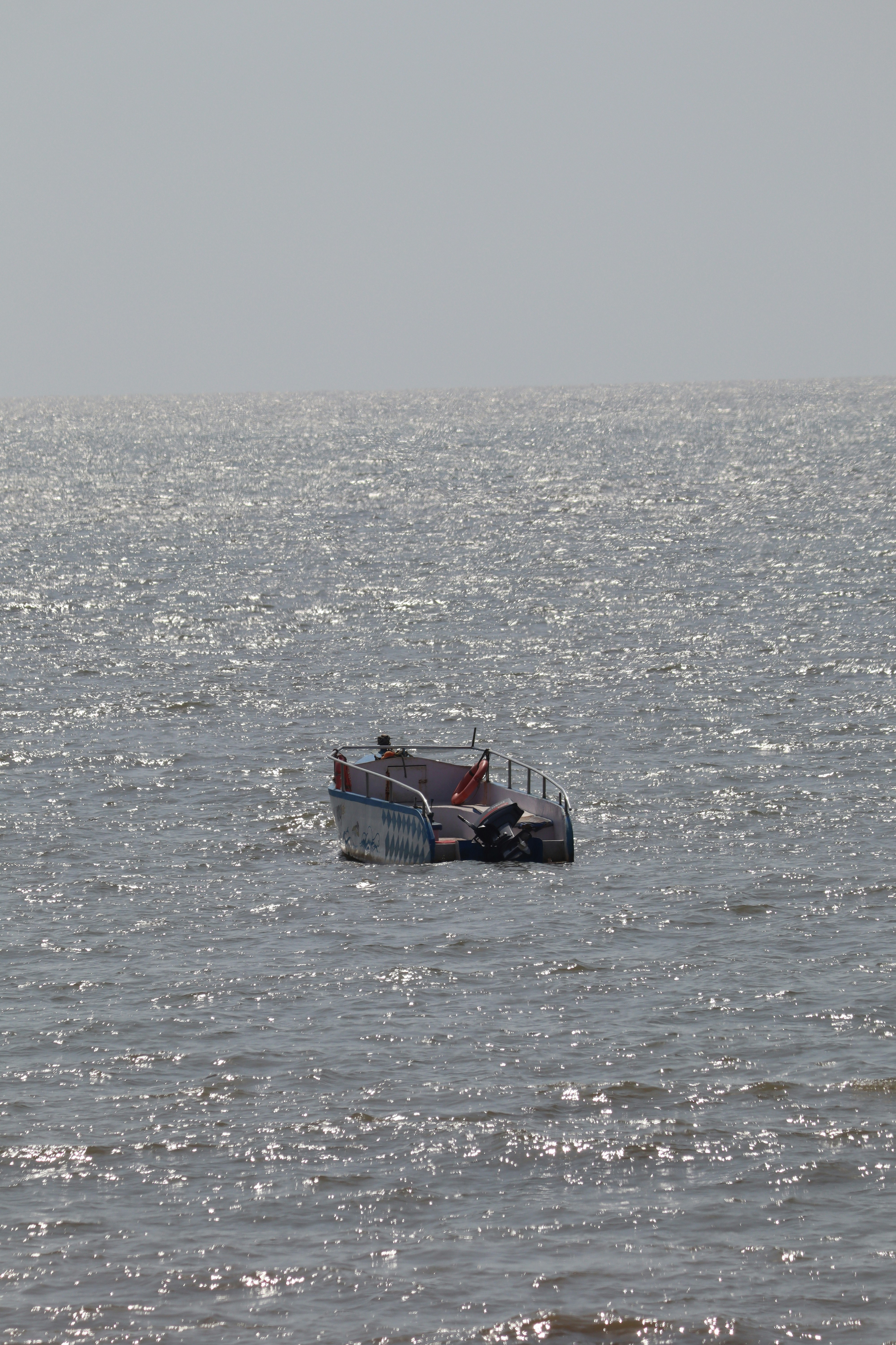 Small passenger boat rides in calm sea under bright glare; distant horizon and sparkling water dominate the frame.