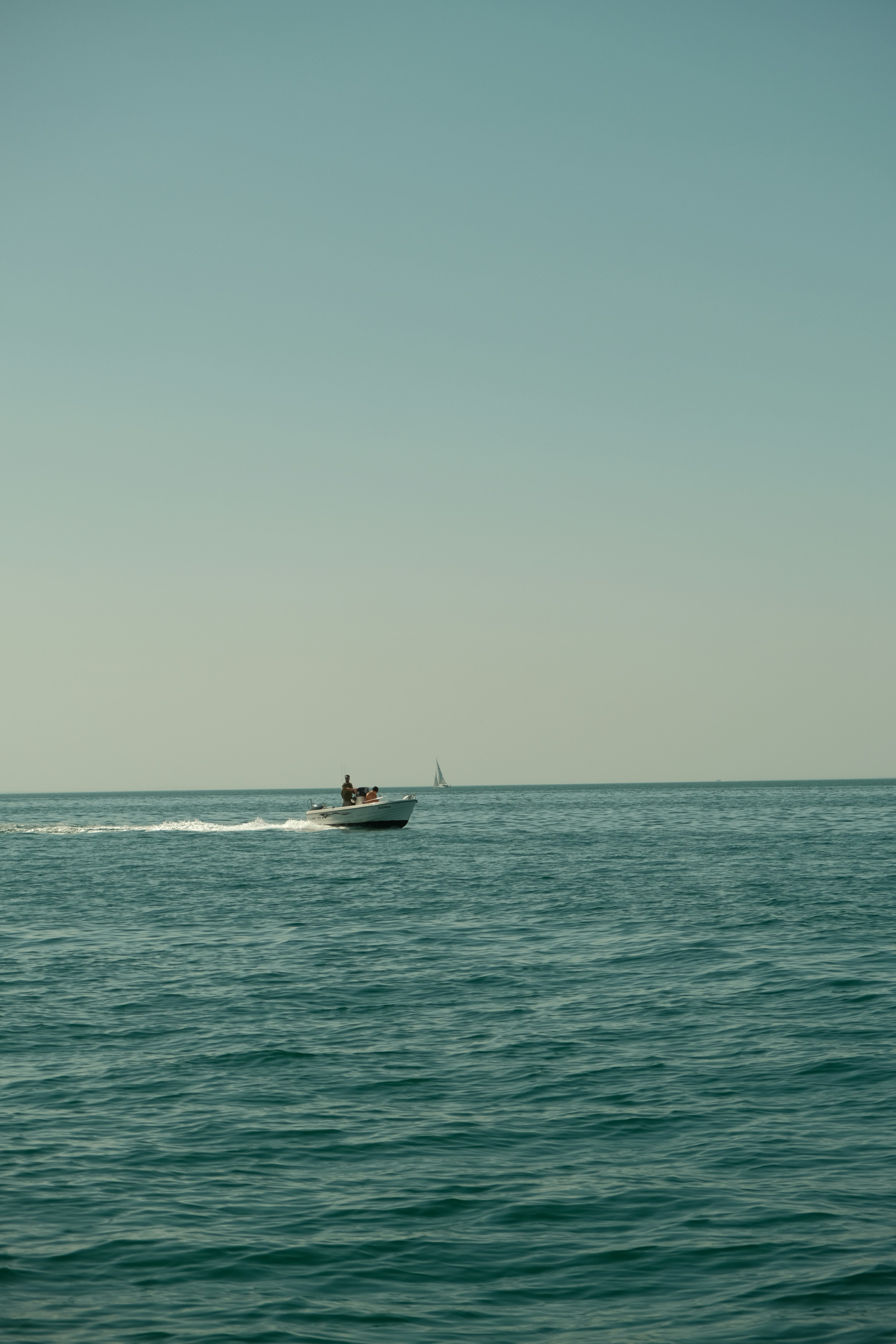 Sea Dawn: A lone speedboat skims the horizon under a tranquil, pale-sky calm
