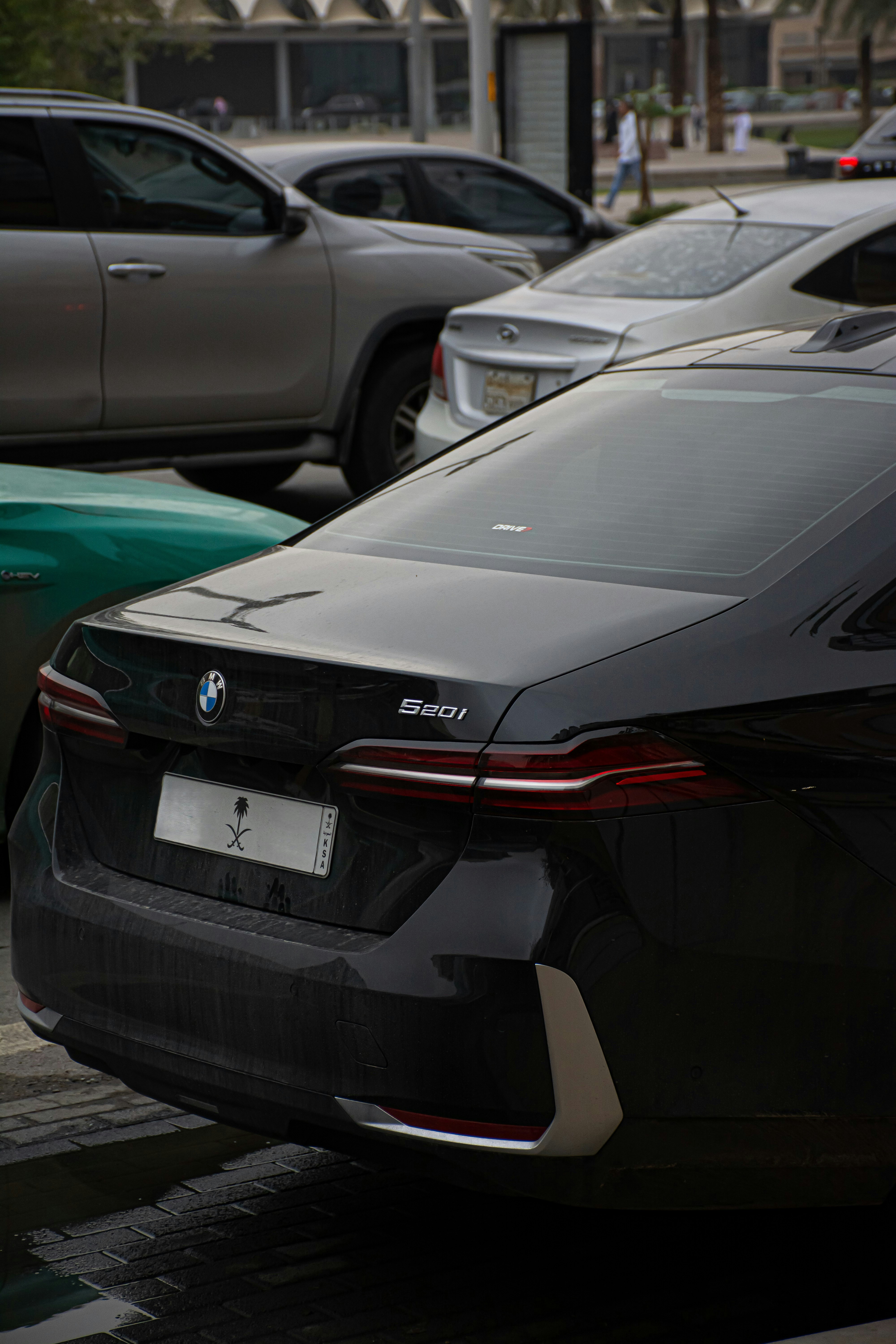 Dark BMW 520i dominates the frame with other parked cars in the background, highlighting tail lights and glossy surfaces.