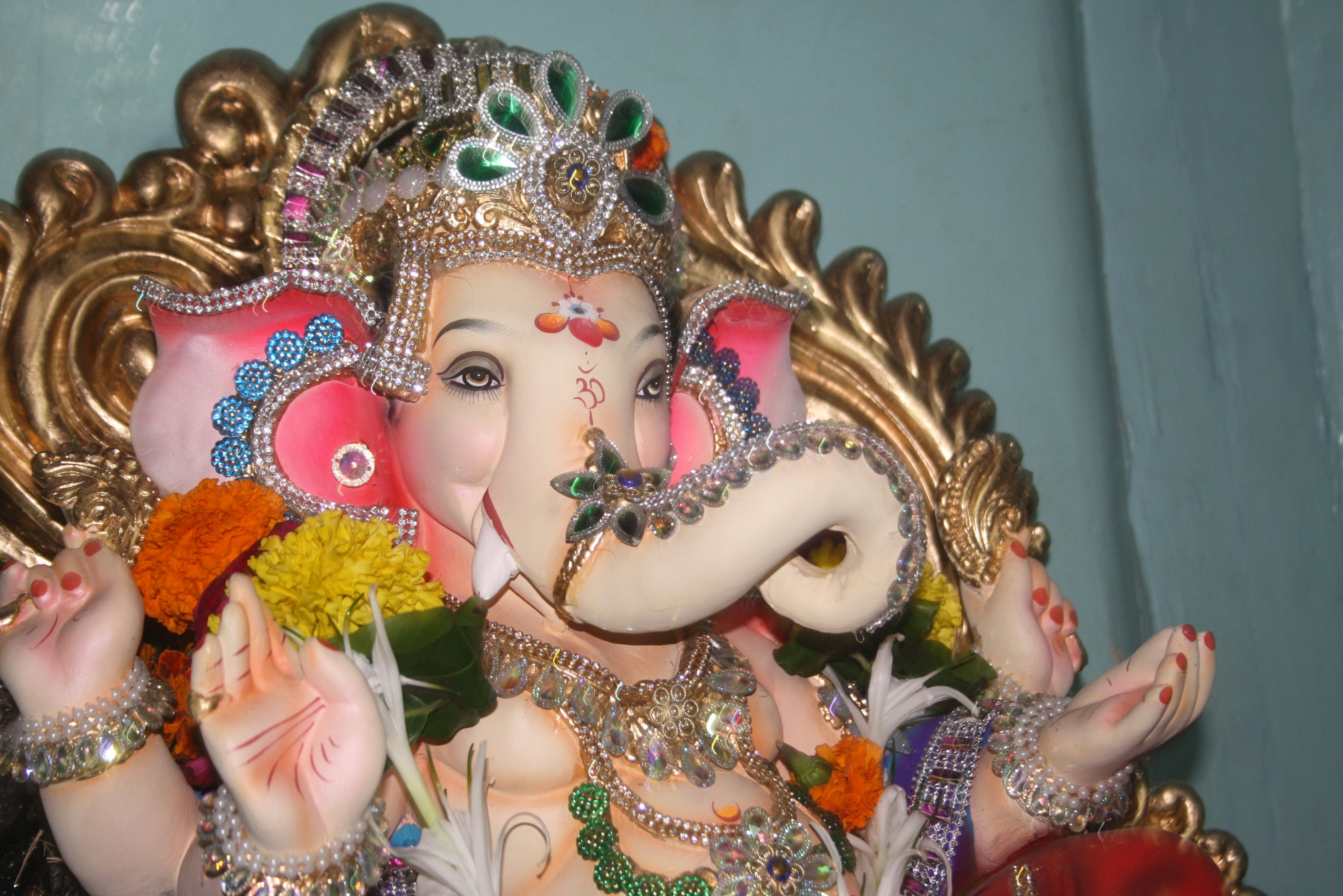 Intricately adorned Ganesh idol with vibrant jewelry, marigolds and lilies, captured in soft indoor lighting.