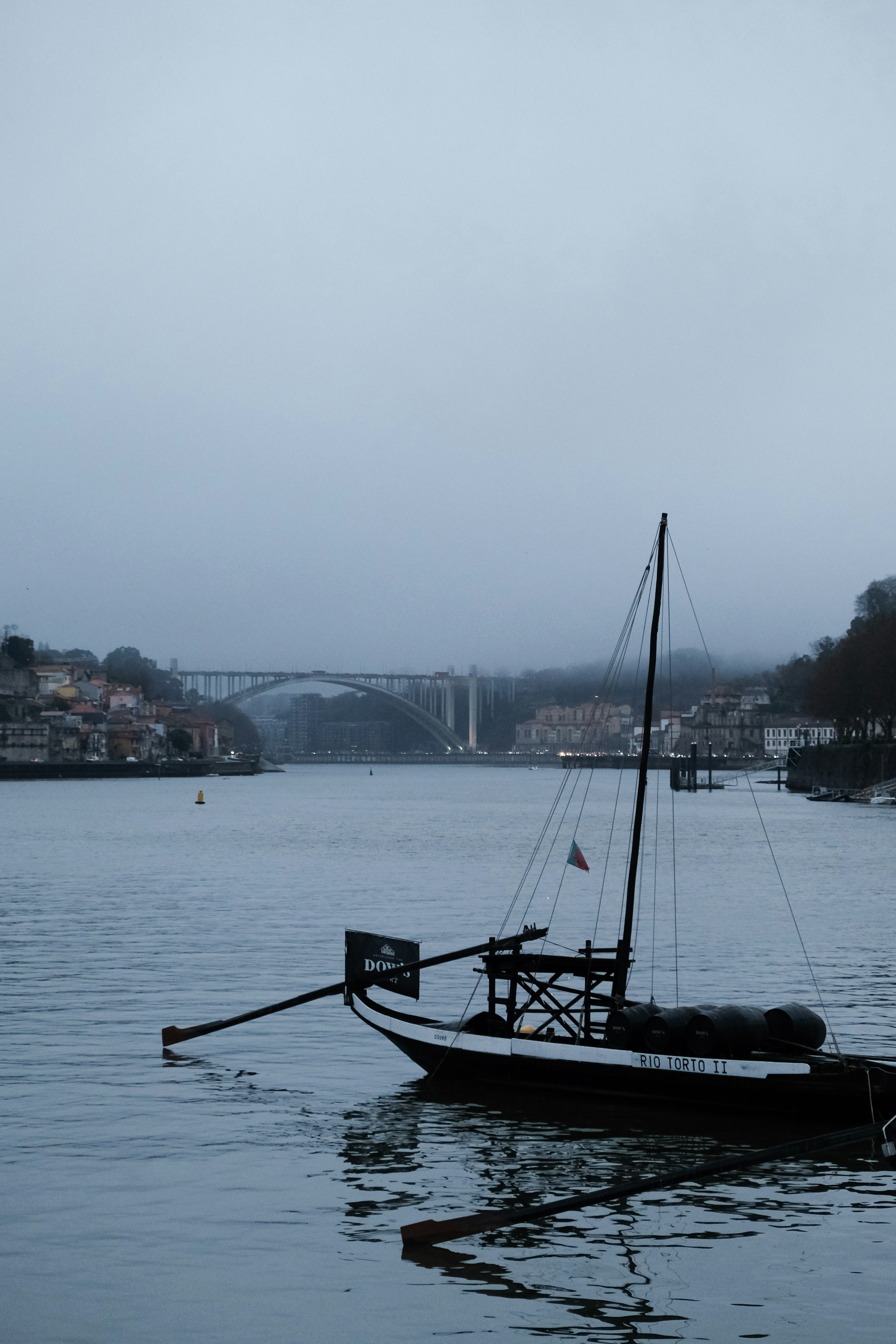 Mooring in a Mist: A Tranquil River Scene with a Sailboat at Dusk