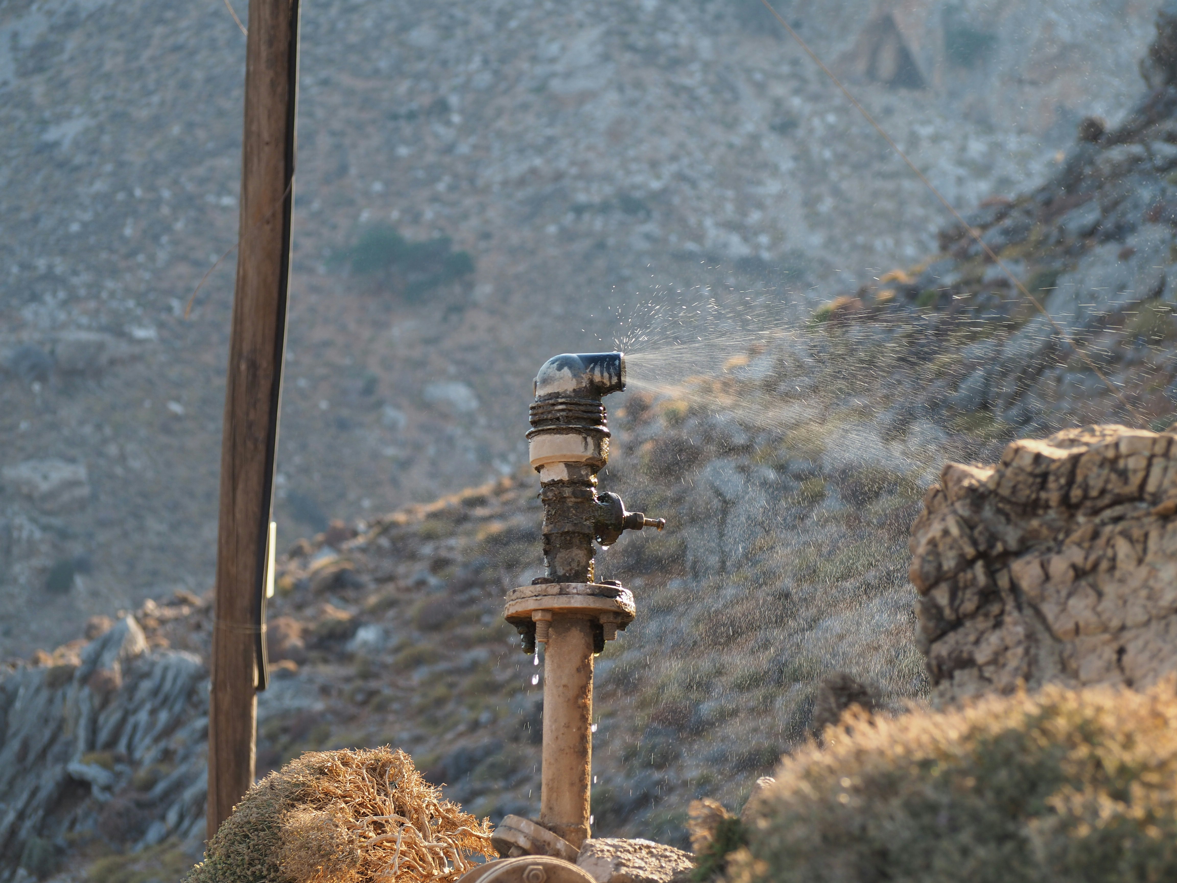 Aweathered water spigot in a sunlit rocky landscape