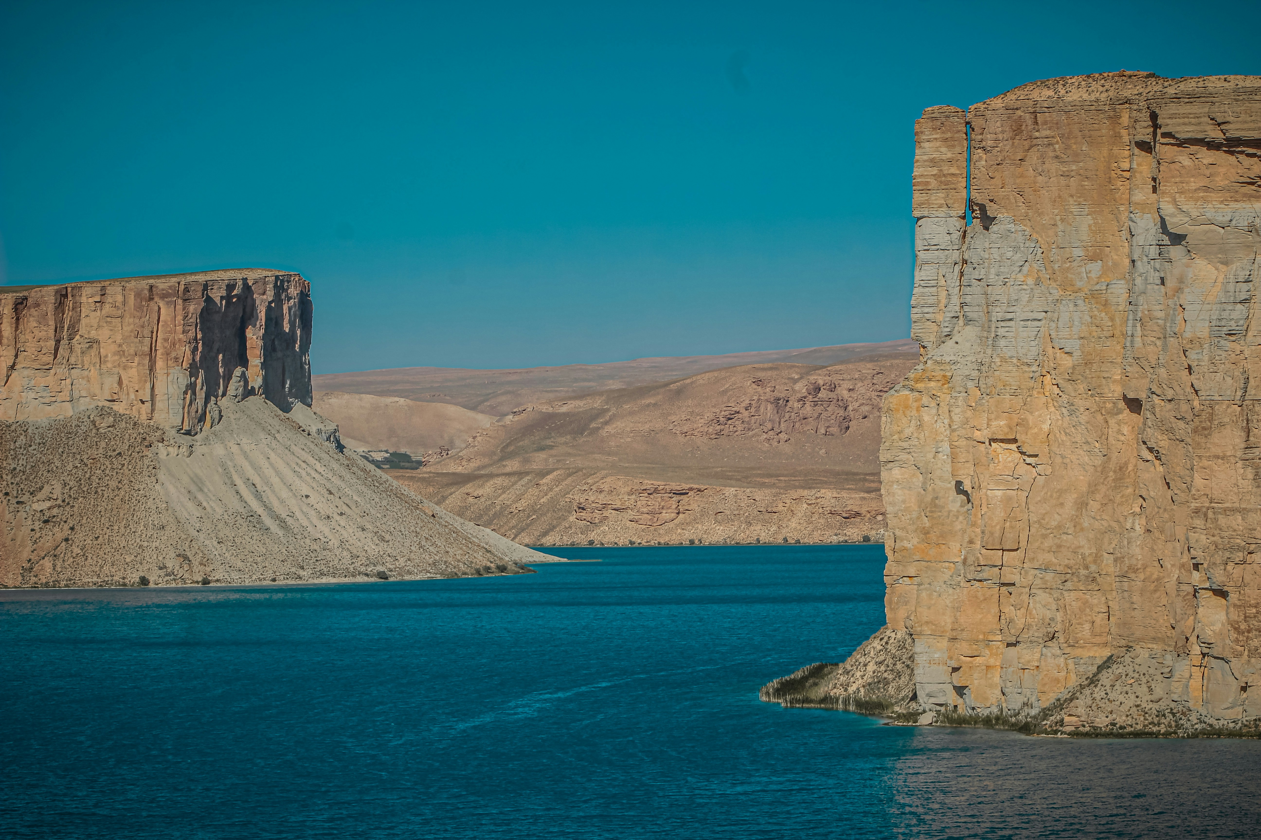 Bold sandstone cliffs rise from a calm blue body of water, with arid canyon walls extending into the distance.