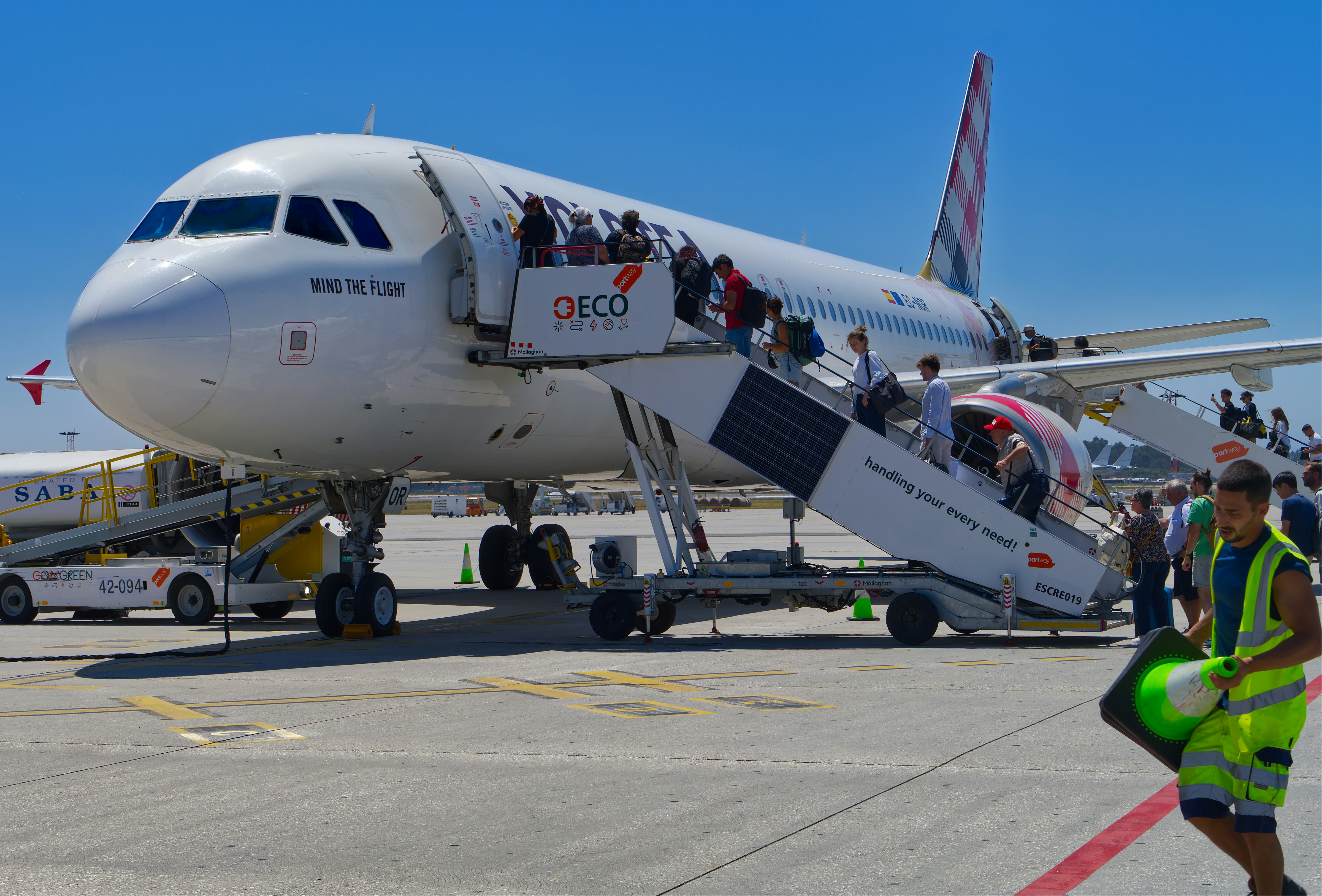 Passenger boarding the aircraft: stairs, ramp, and ground crew at a sunlit tarmac