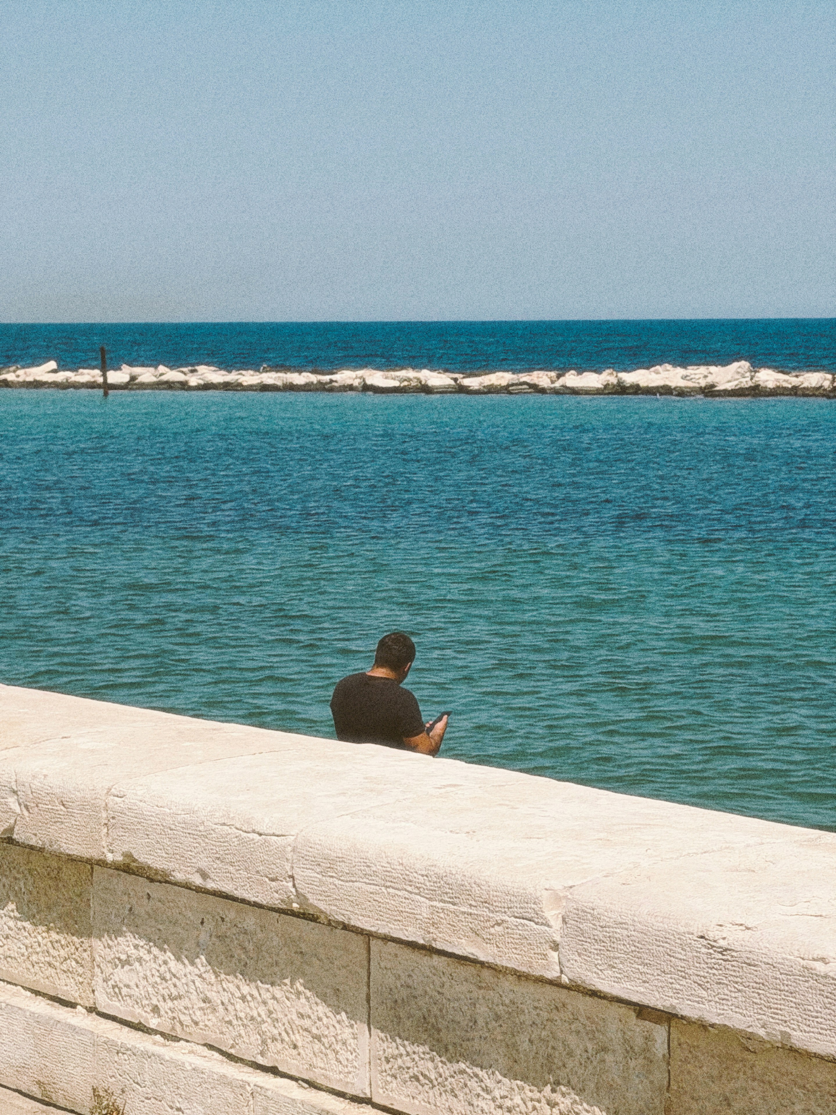 Seaside Quiet: A lone figure gazes toward the horizon from a sunlit seawall