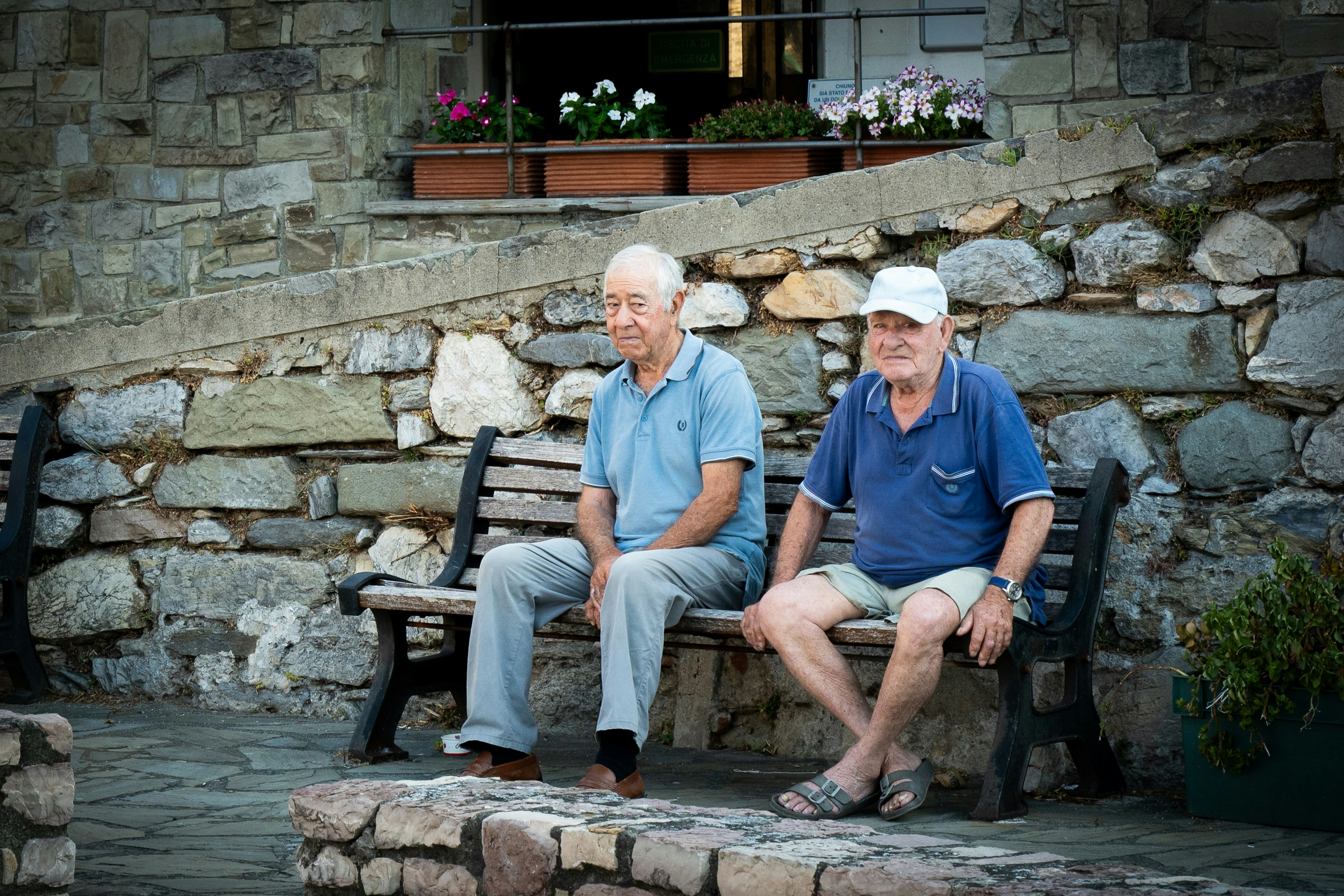 Stone bench, shared quiet: two aging friends in a sunlit courtyard
